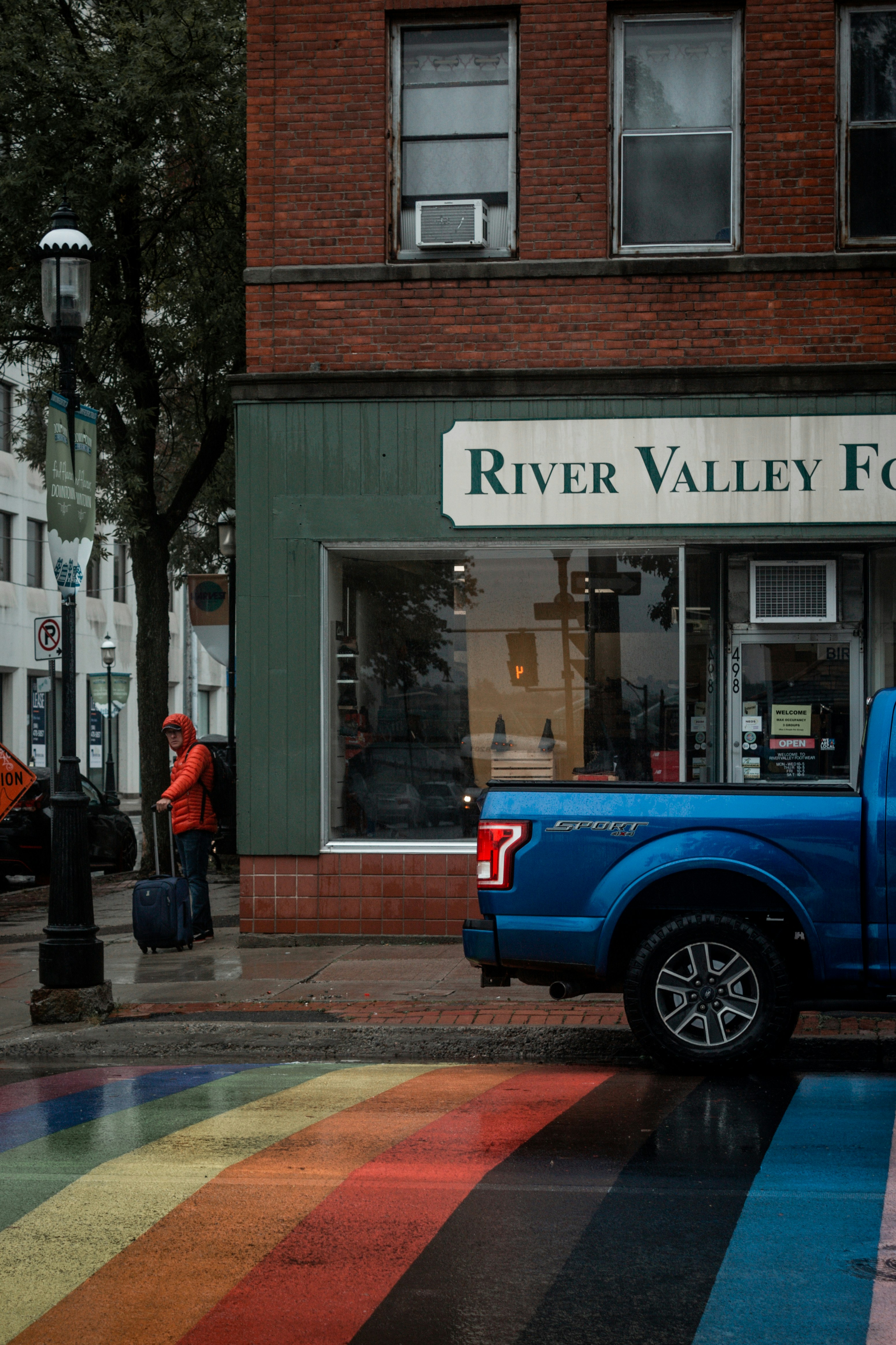 Blue Pickup Anchored by a Rainbow Crosswalk at River Valley Storefront