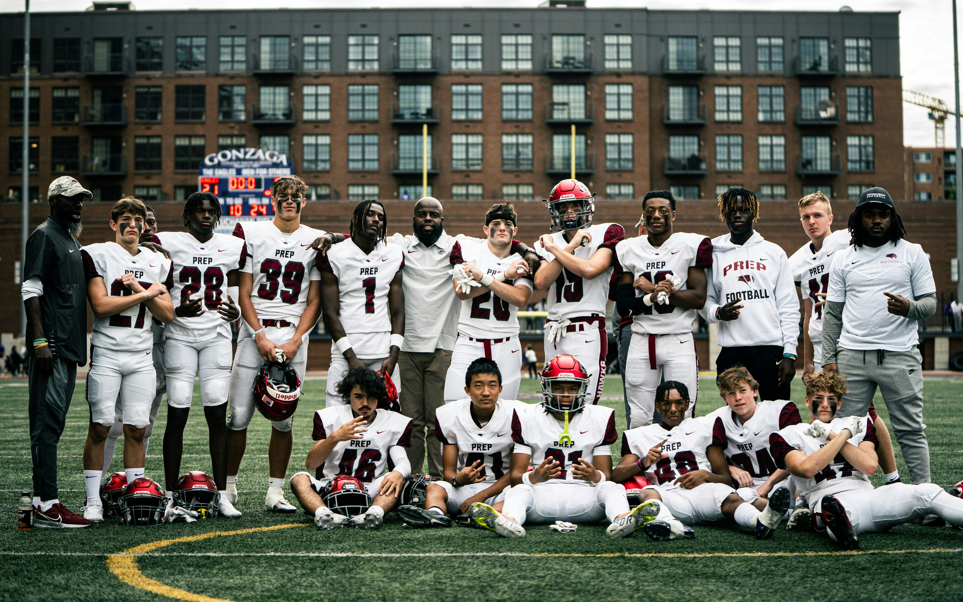 Football team posing together on the field, showcasing camaraderie and team spirit. The players wear matching uniforms and helmets, with a city backdrop hinting at their competitive environment.