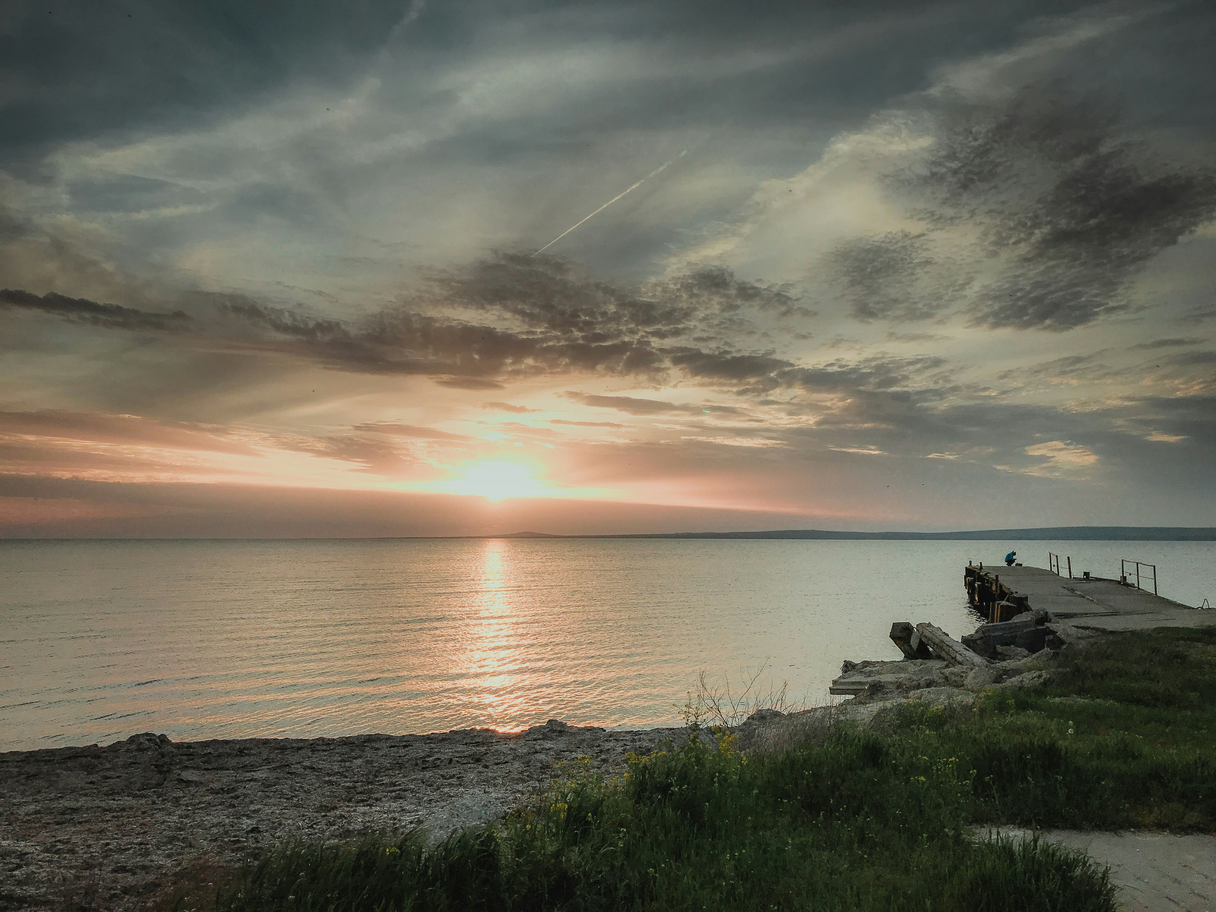 Sunset over calm sea with dramatic clouds and weathered pier.