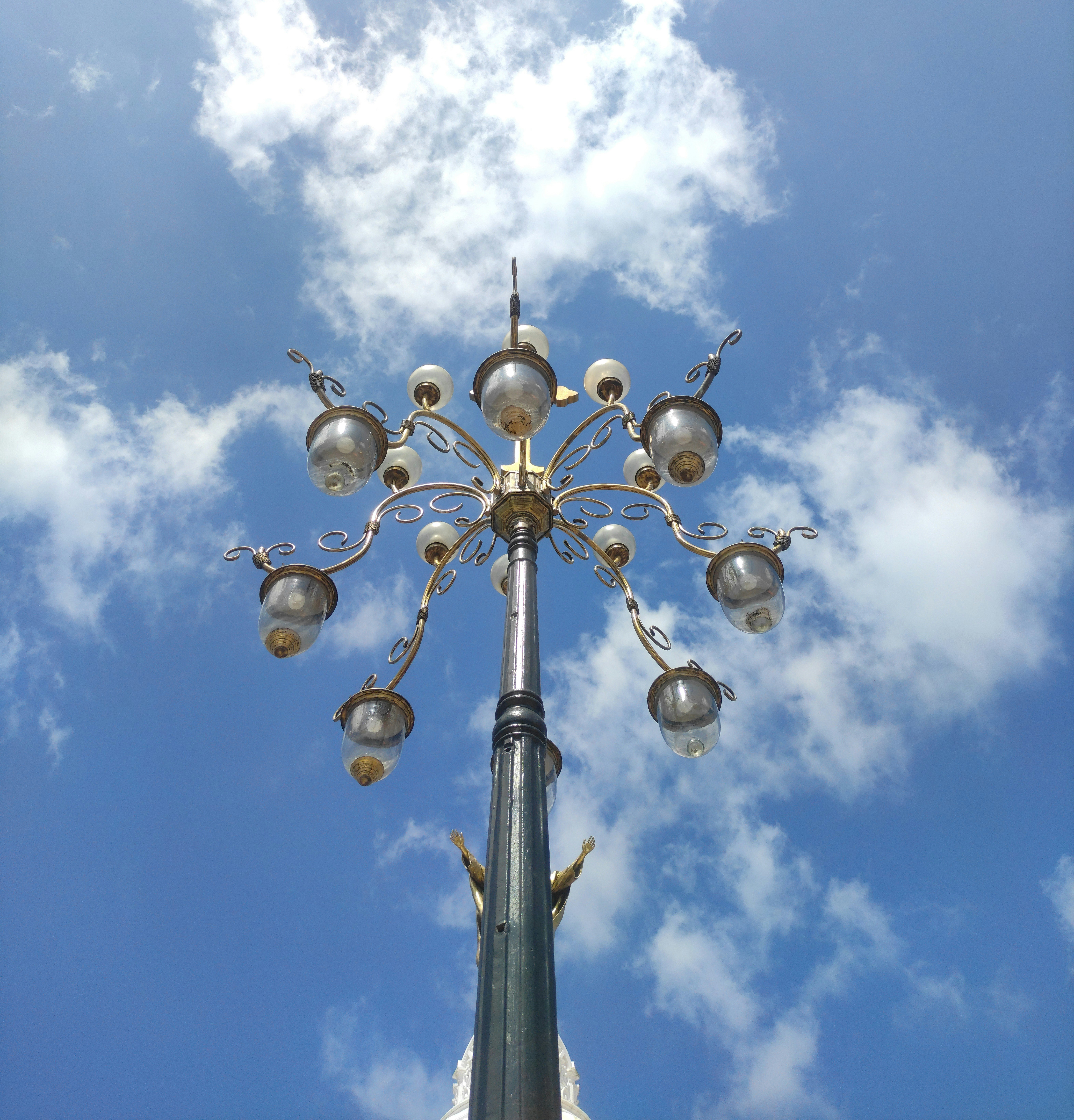 Ornate street lamp with multiple glass globes against a bright blue sky with fluffy clouds.