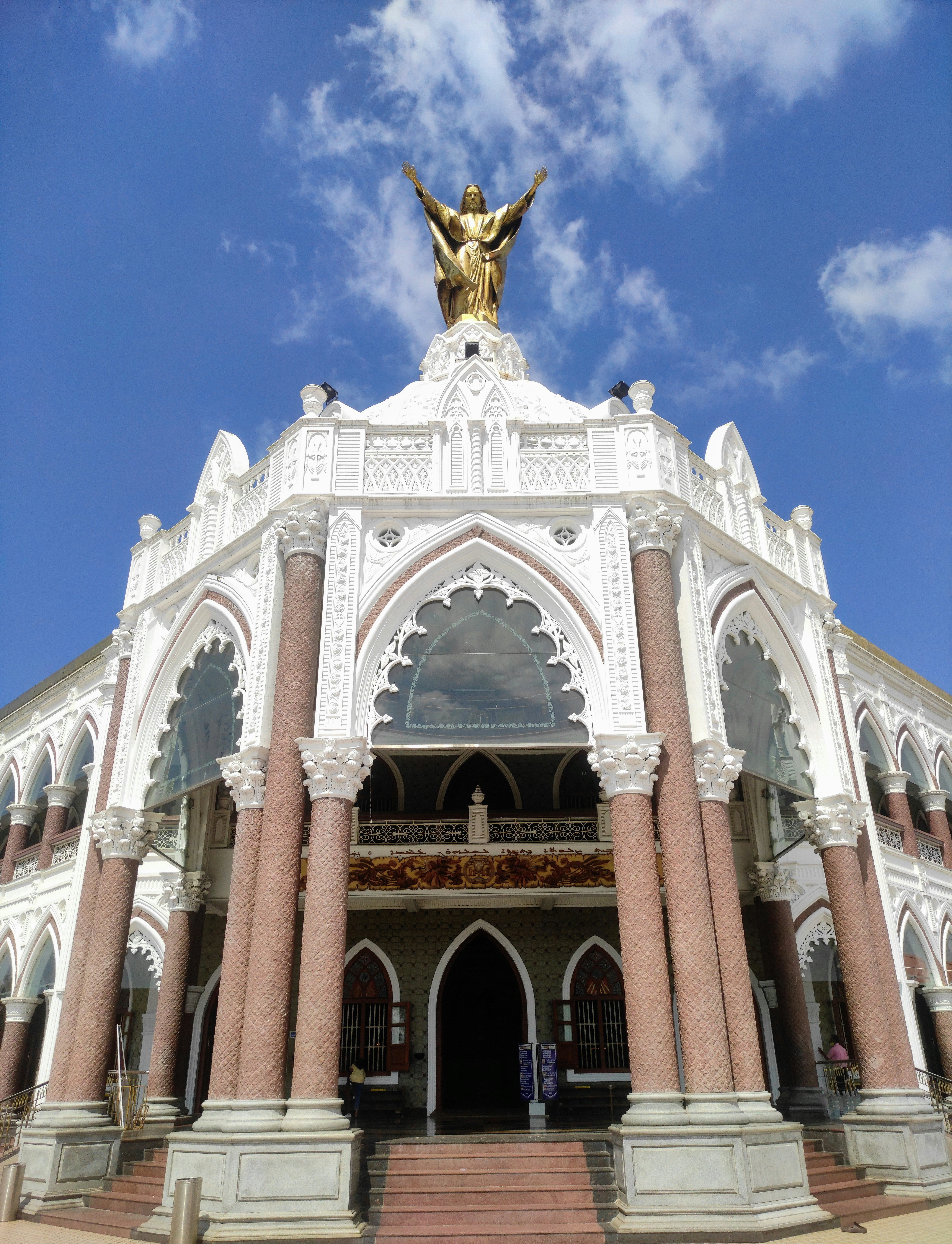 A majestic church facade with intricate arches and a towering golden statue of Christ, set against a vibrant blue sky.