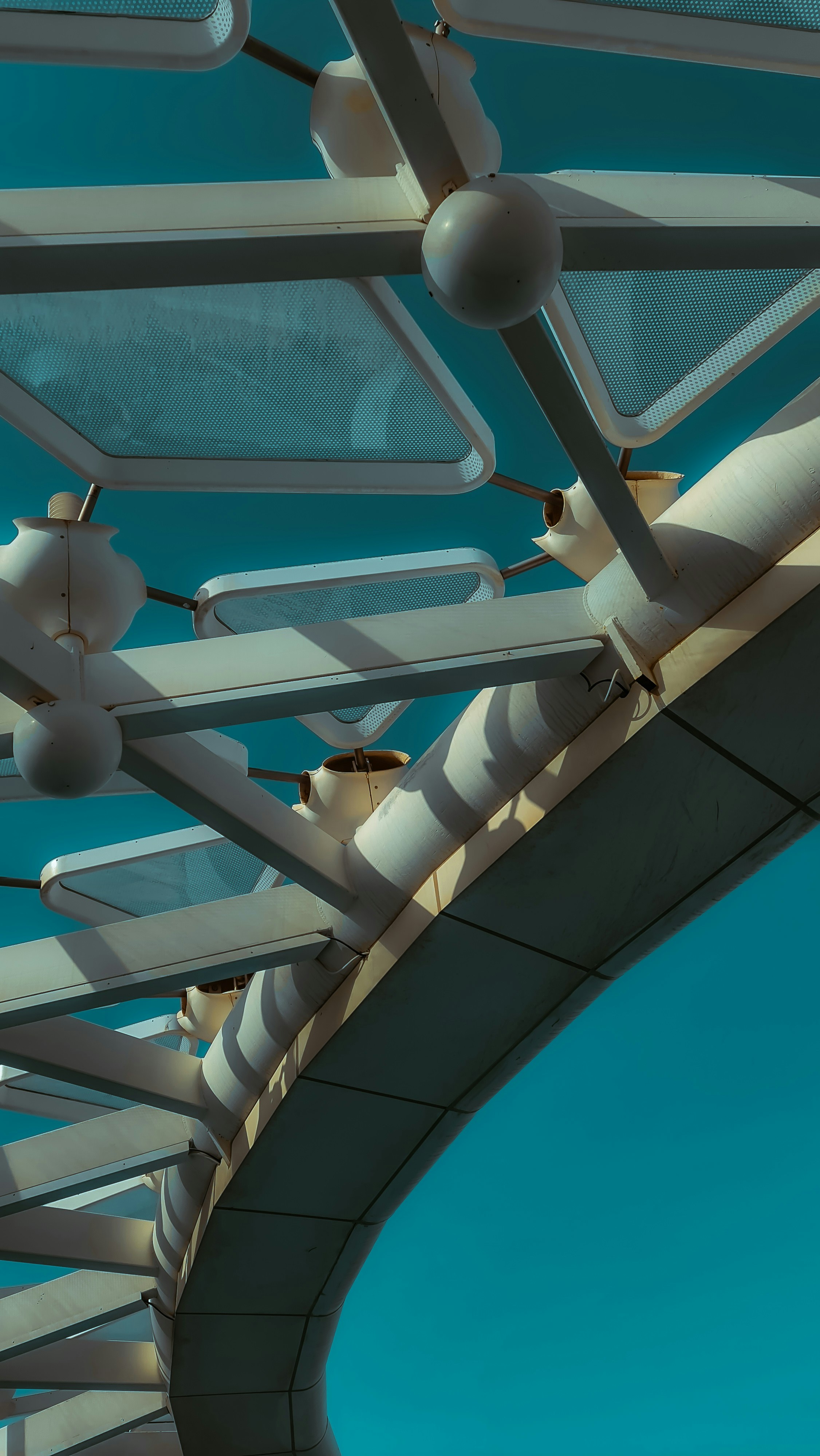 Curved architectural structure with intricate patterns and shadows against a clear blue sky.