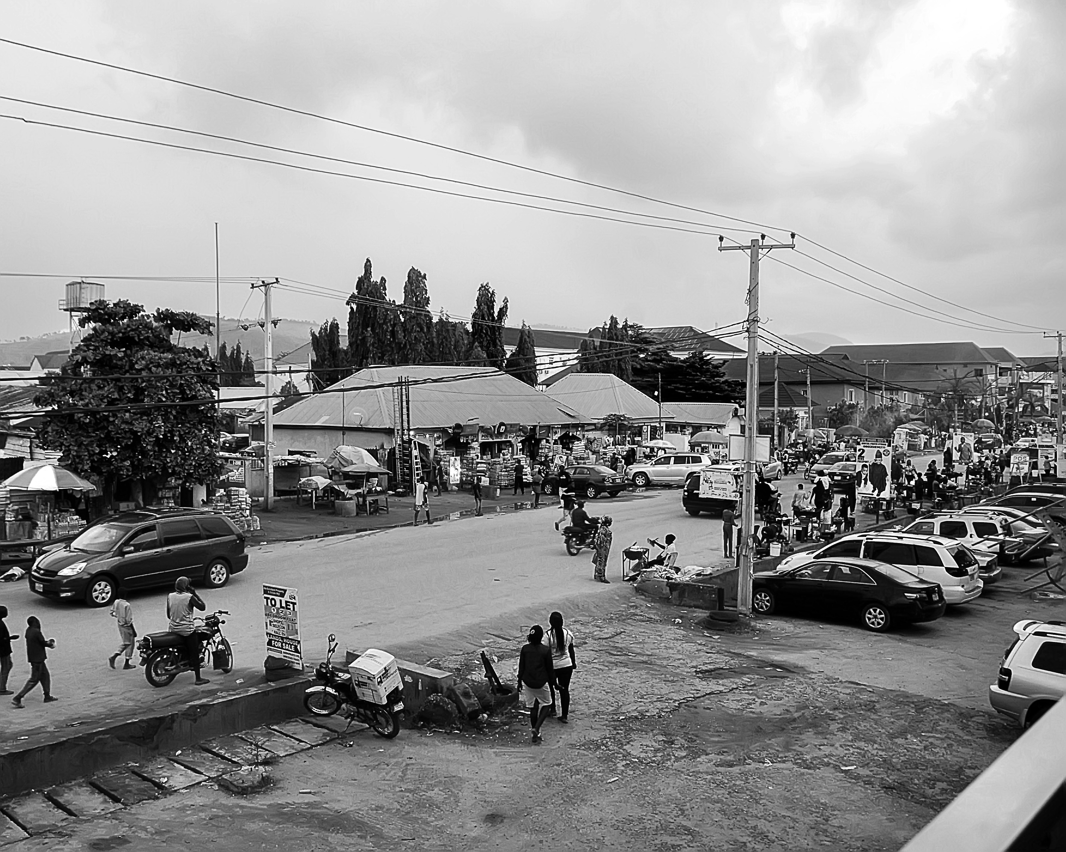 Busy street scene with people and cars under a cloudy sky.