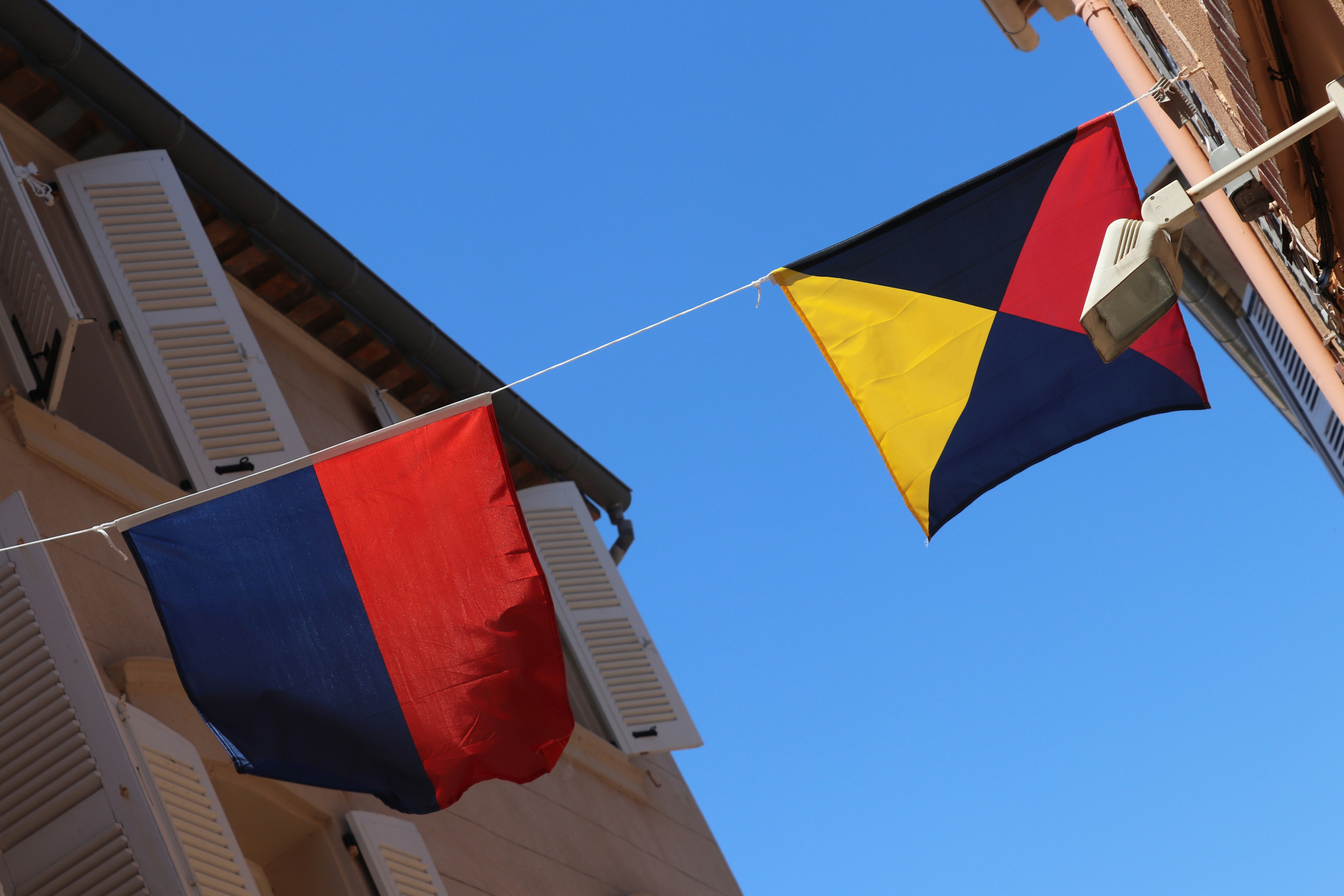 A couple of flags flying in the air next to a building photo – Free ...