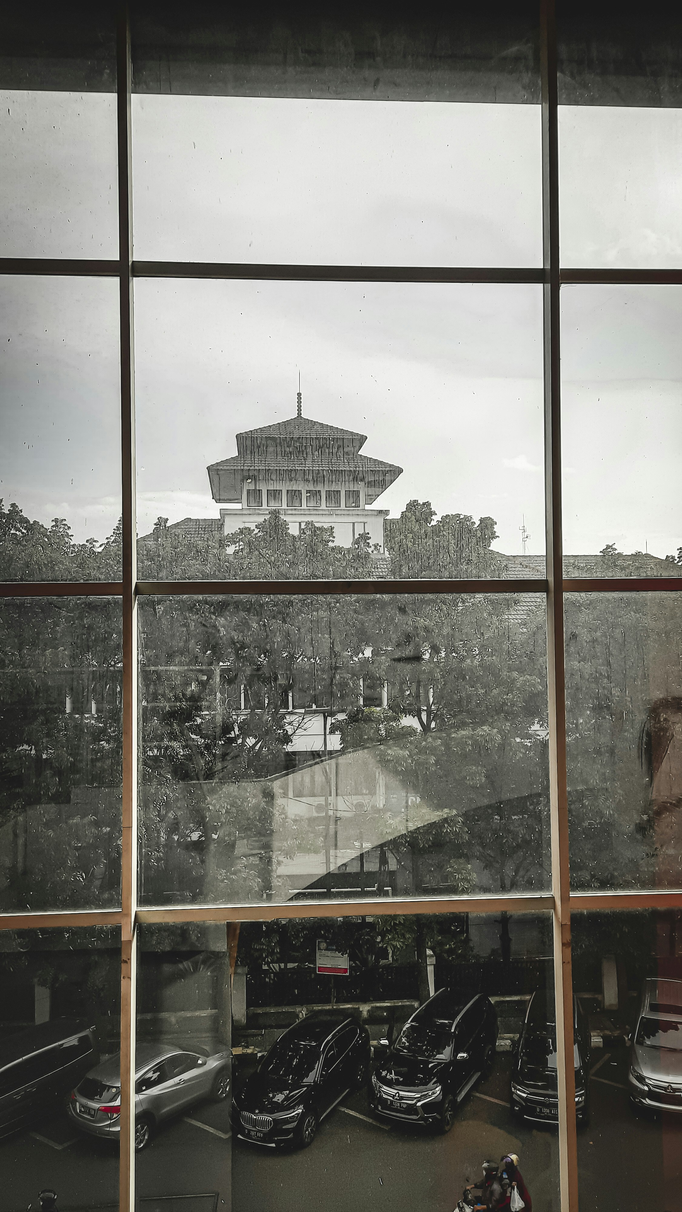 Window-framed view of a pagoda-topped building rising behind trees, with a car-filled lot in the foreground.