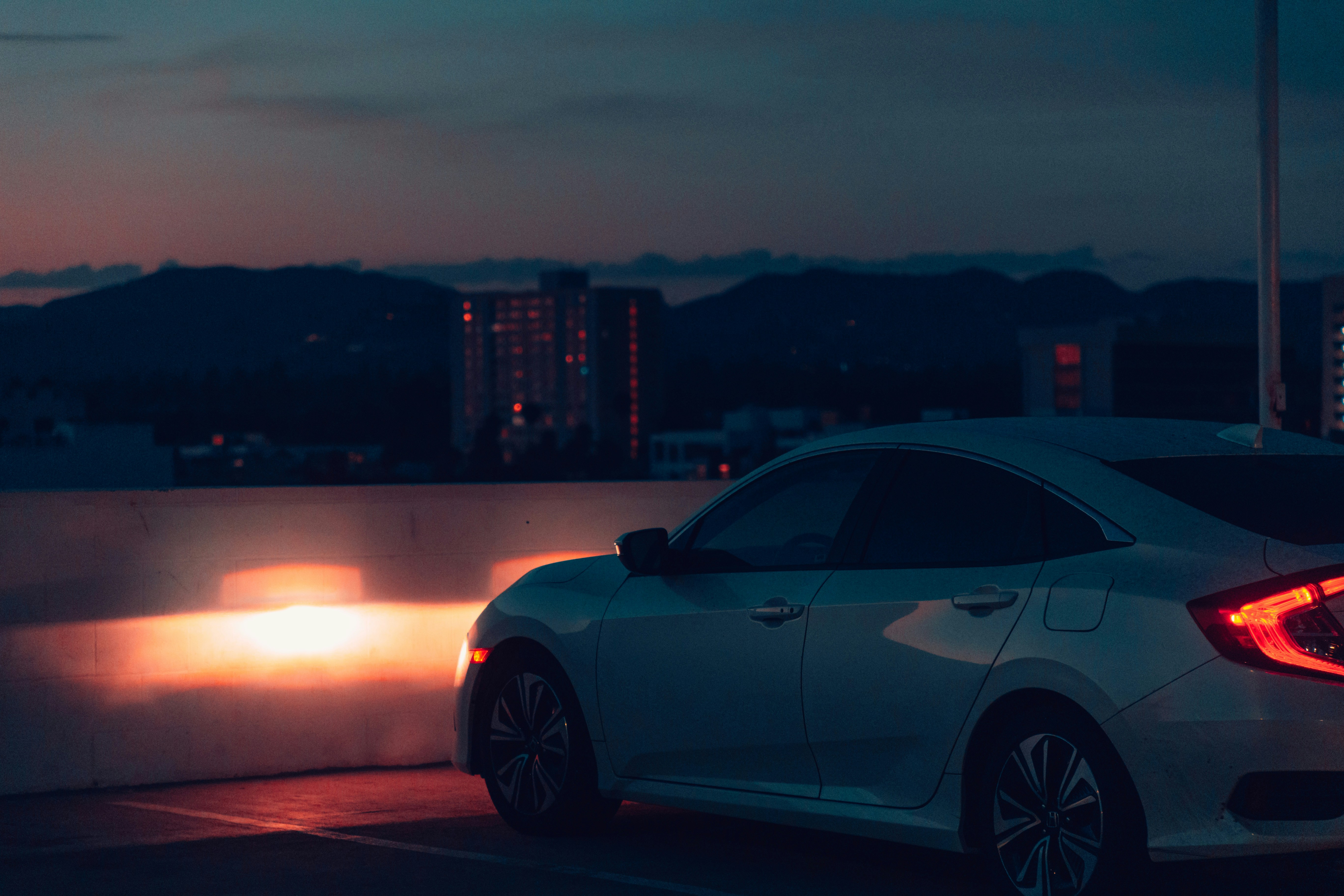 Rooftop Reverie: A White Sedan Amid Blue Hour and Neon City Backdrop