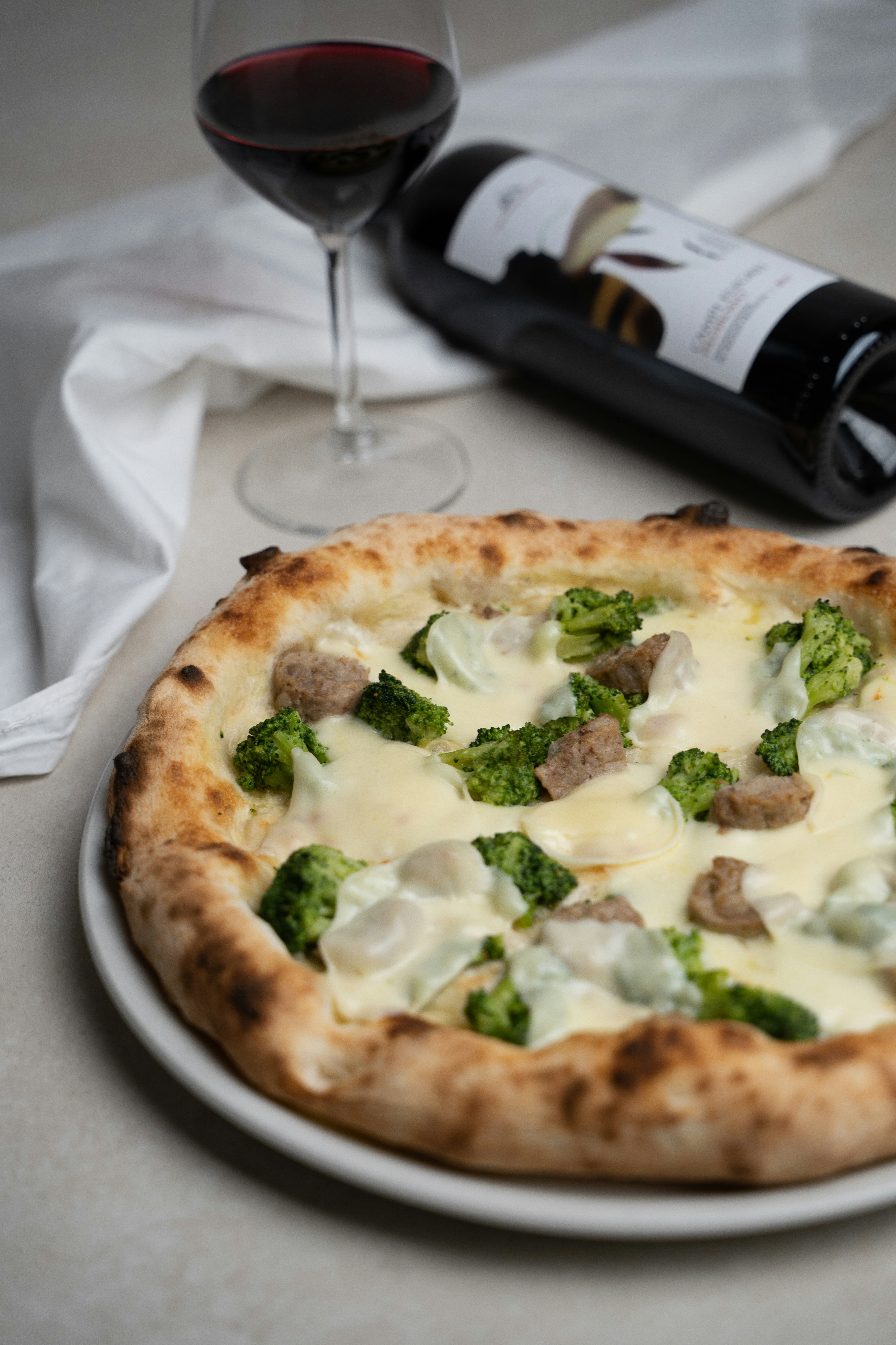 Emerald-Broccoli Sausage Pizza Framed by a Quiet Red-Wine Moment