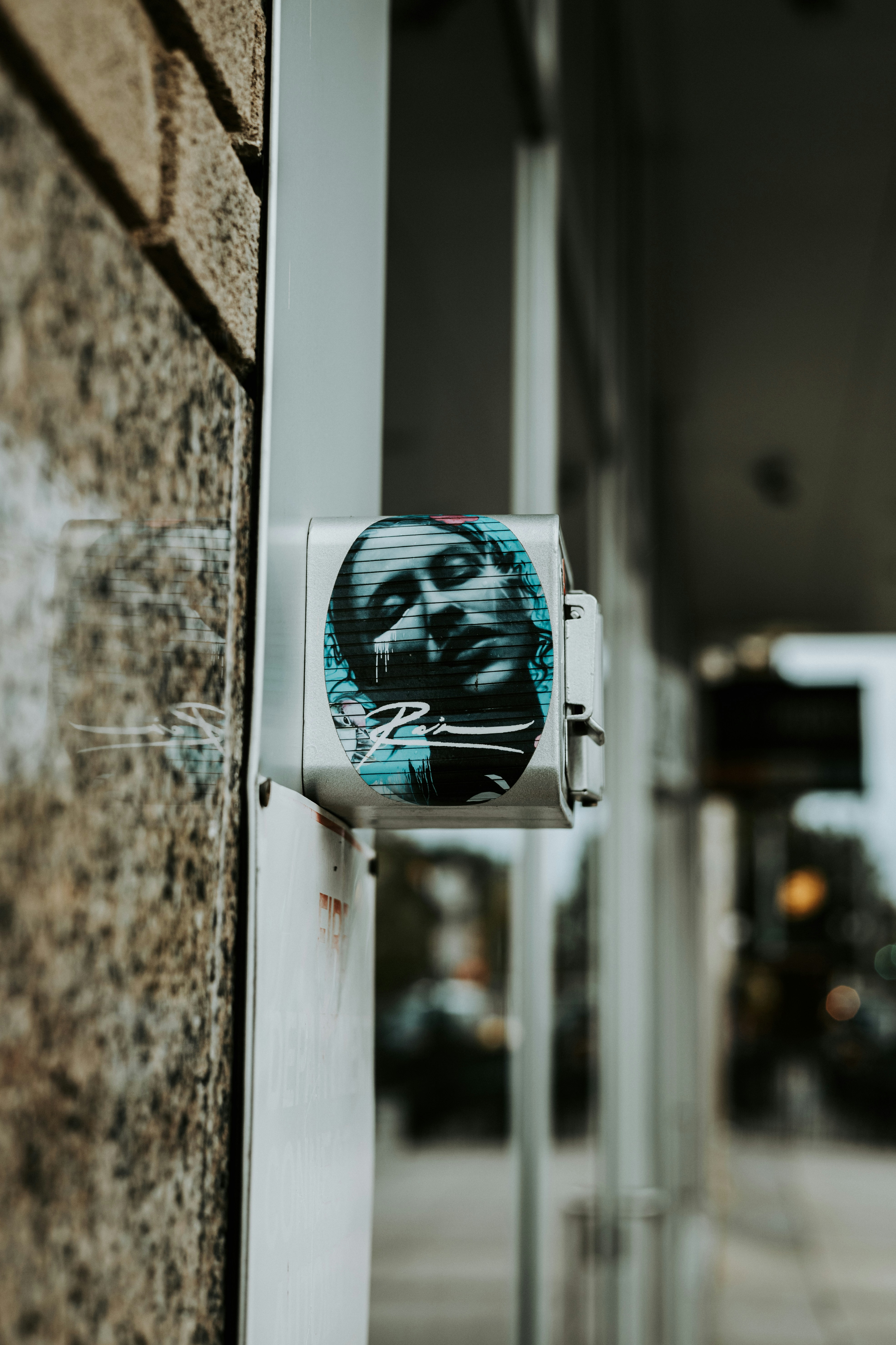 Cyan Portrait on Brick and Glass: Circular Sticker on a Metal Box