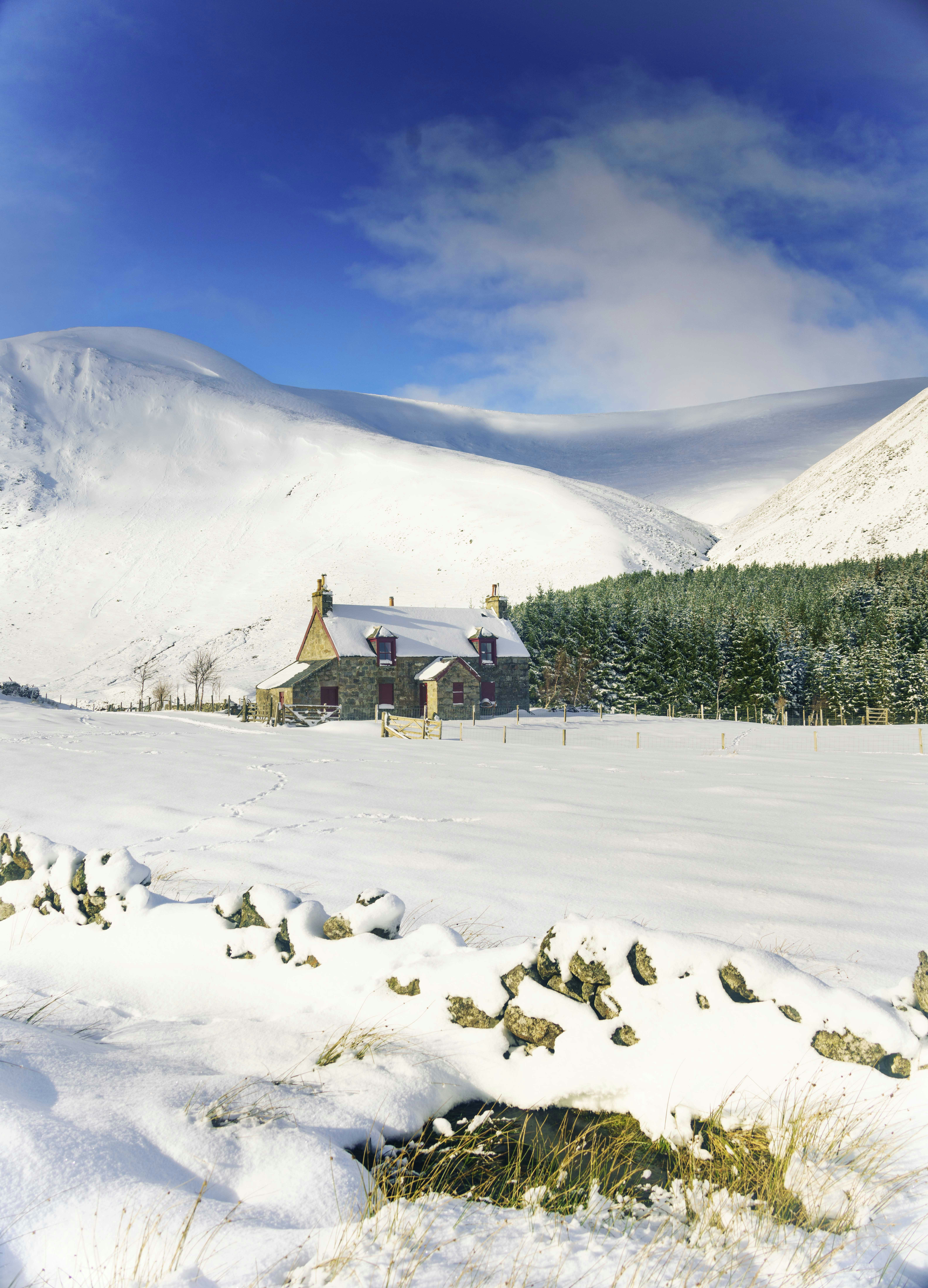 a remote house in the hills around braemar in scotland sits covered in snow in the sunlight