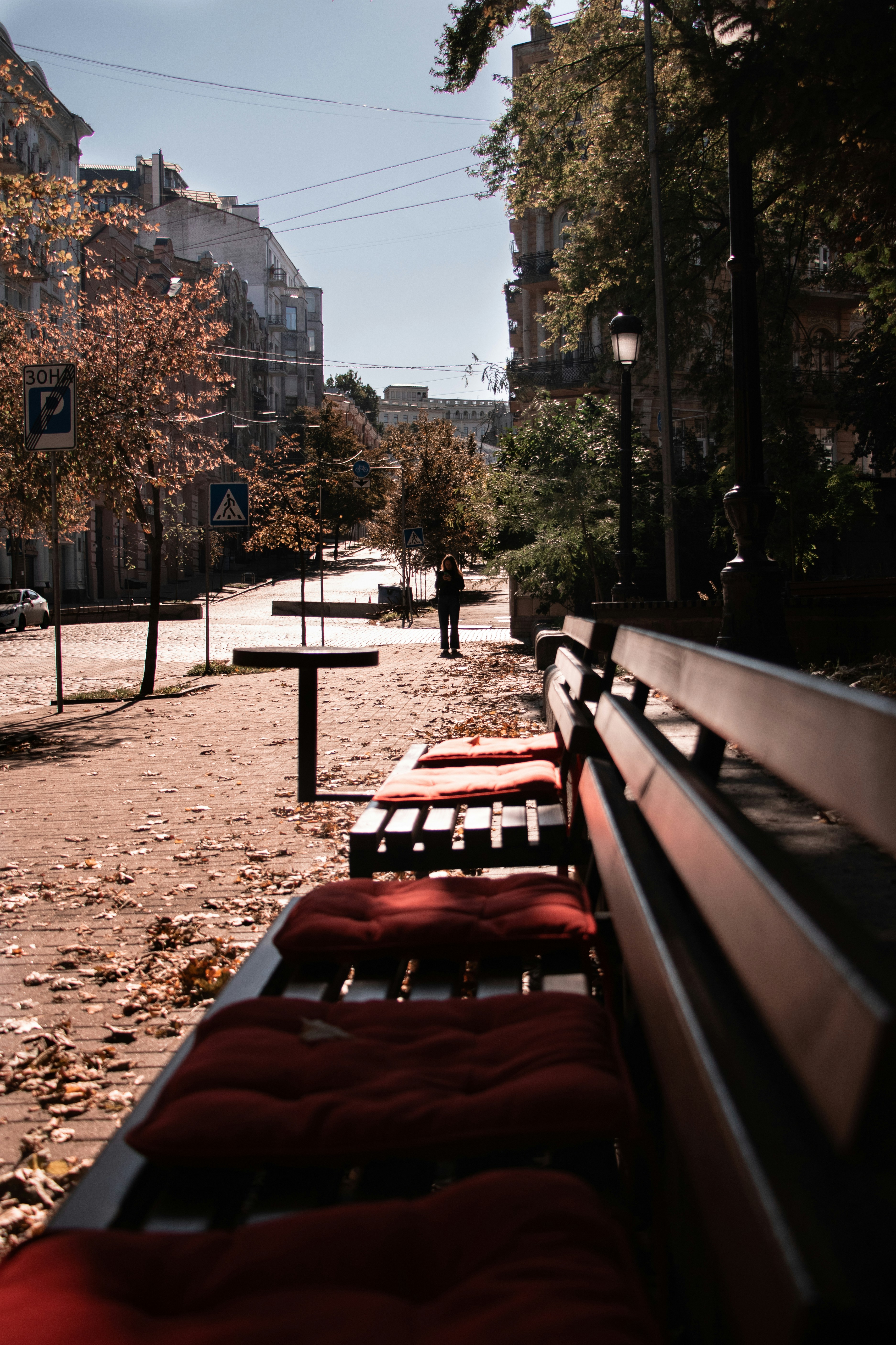 Autumn Light on a City Bench: Red Cushions and a Distant Figure