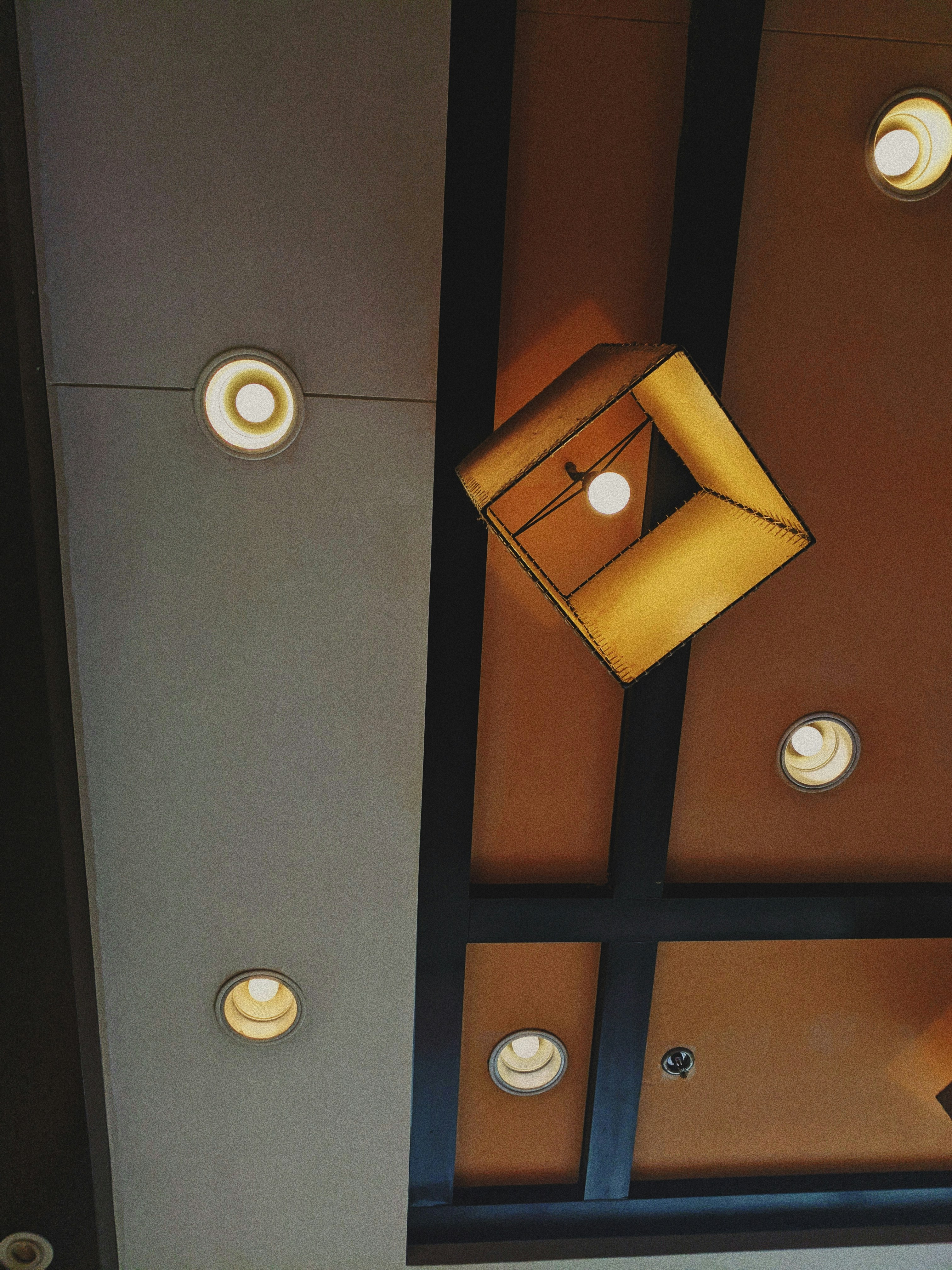 Stylish ceiling featuring a modern light fixture and circular recessed lights against a warm-toned background.