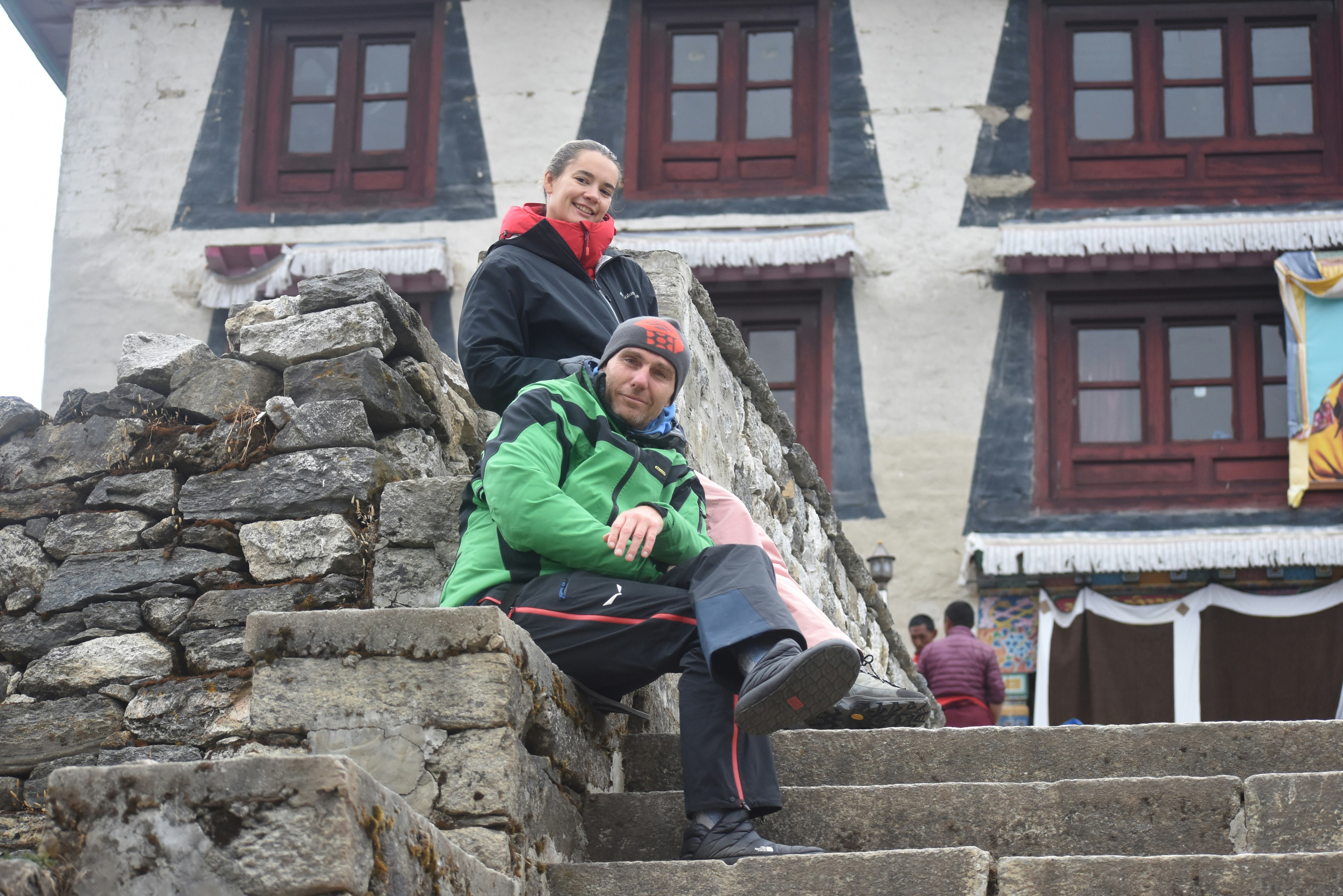 Two hikers rest on ancient stone stairs before a hillside inn