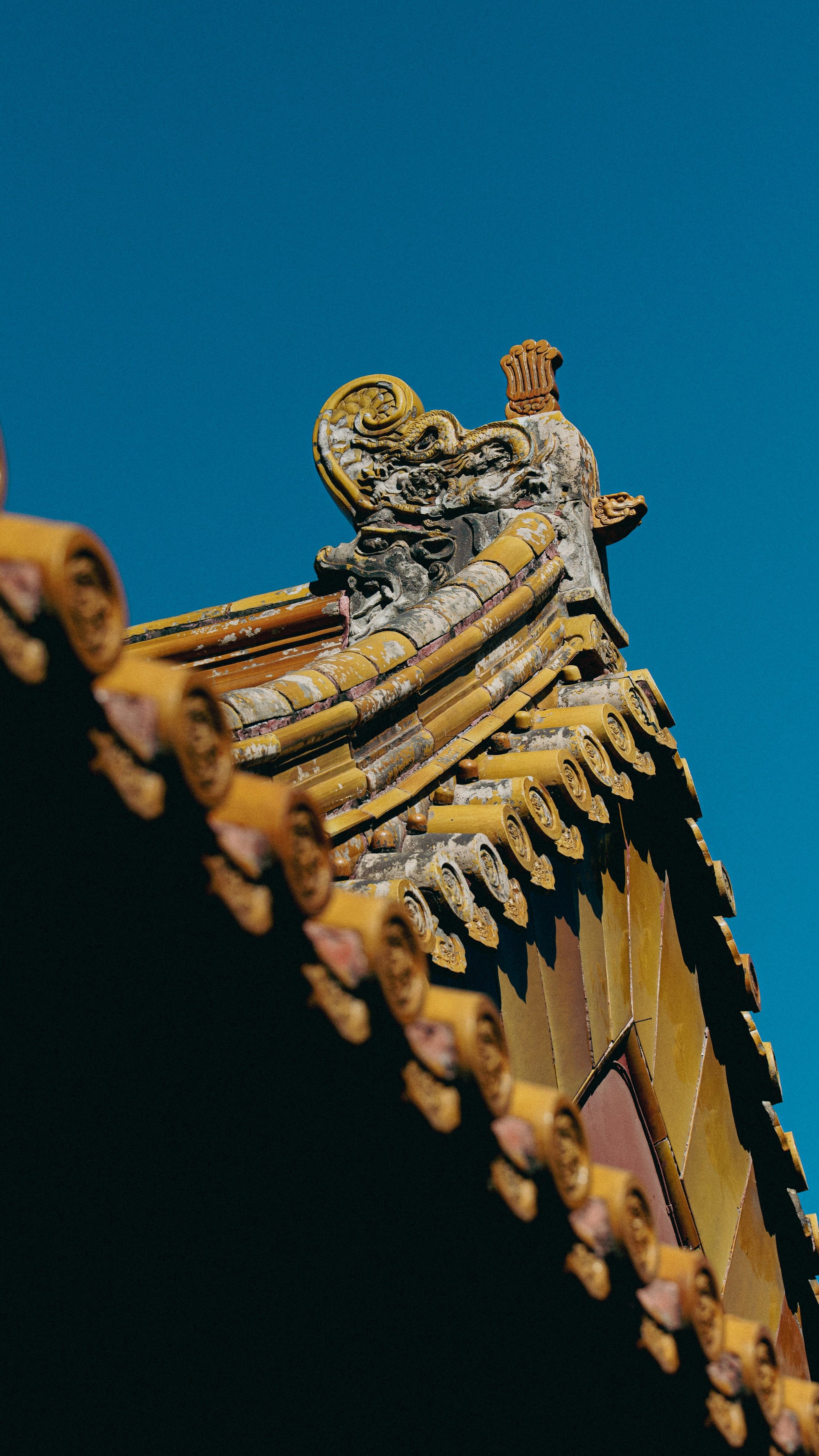 Intricate dragon motif atop a traditional roof against a clear blue sky.