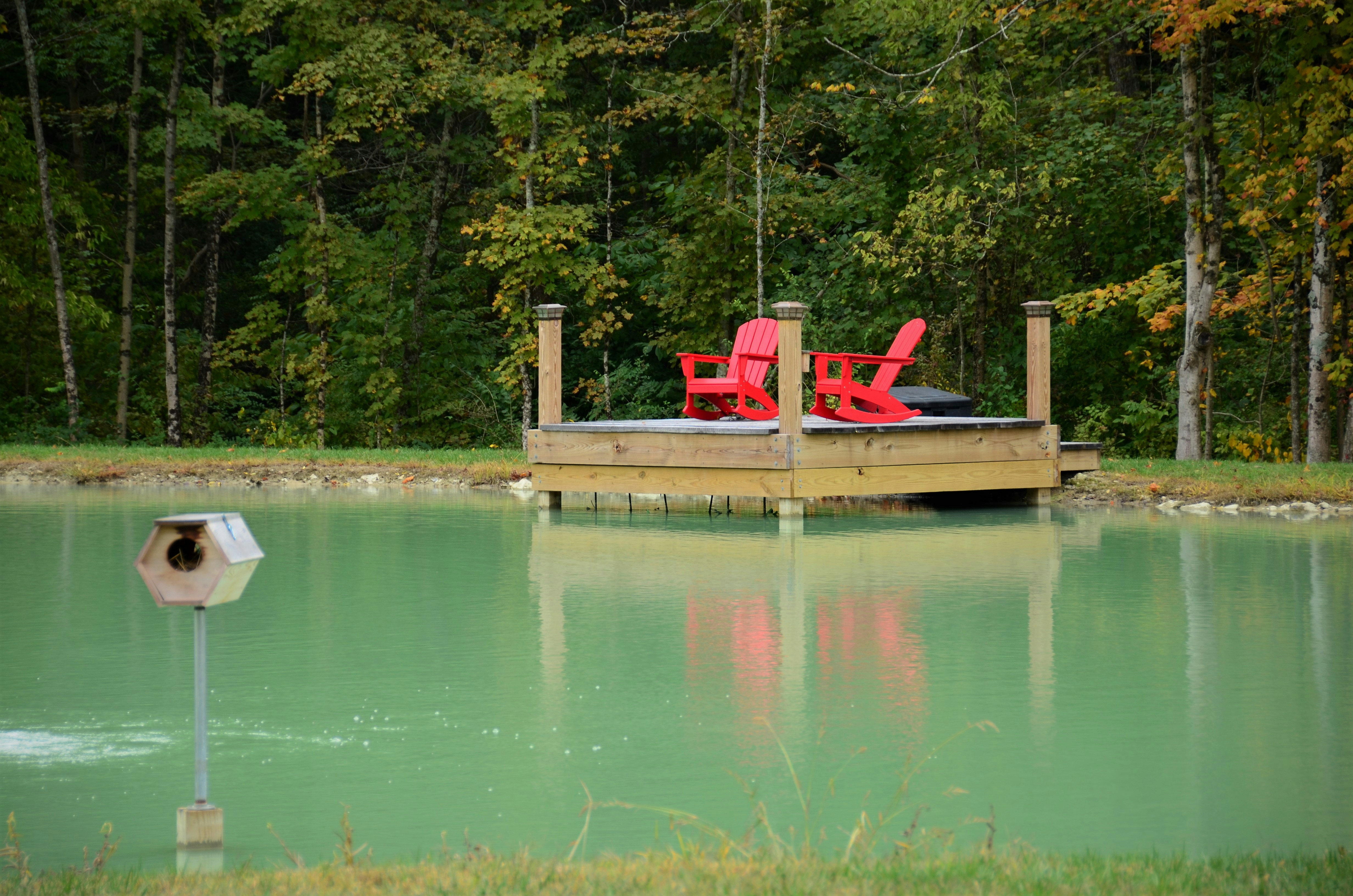 Red Adirondack Chairs Repose on a Deck Over a Turquoise Pond