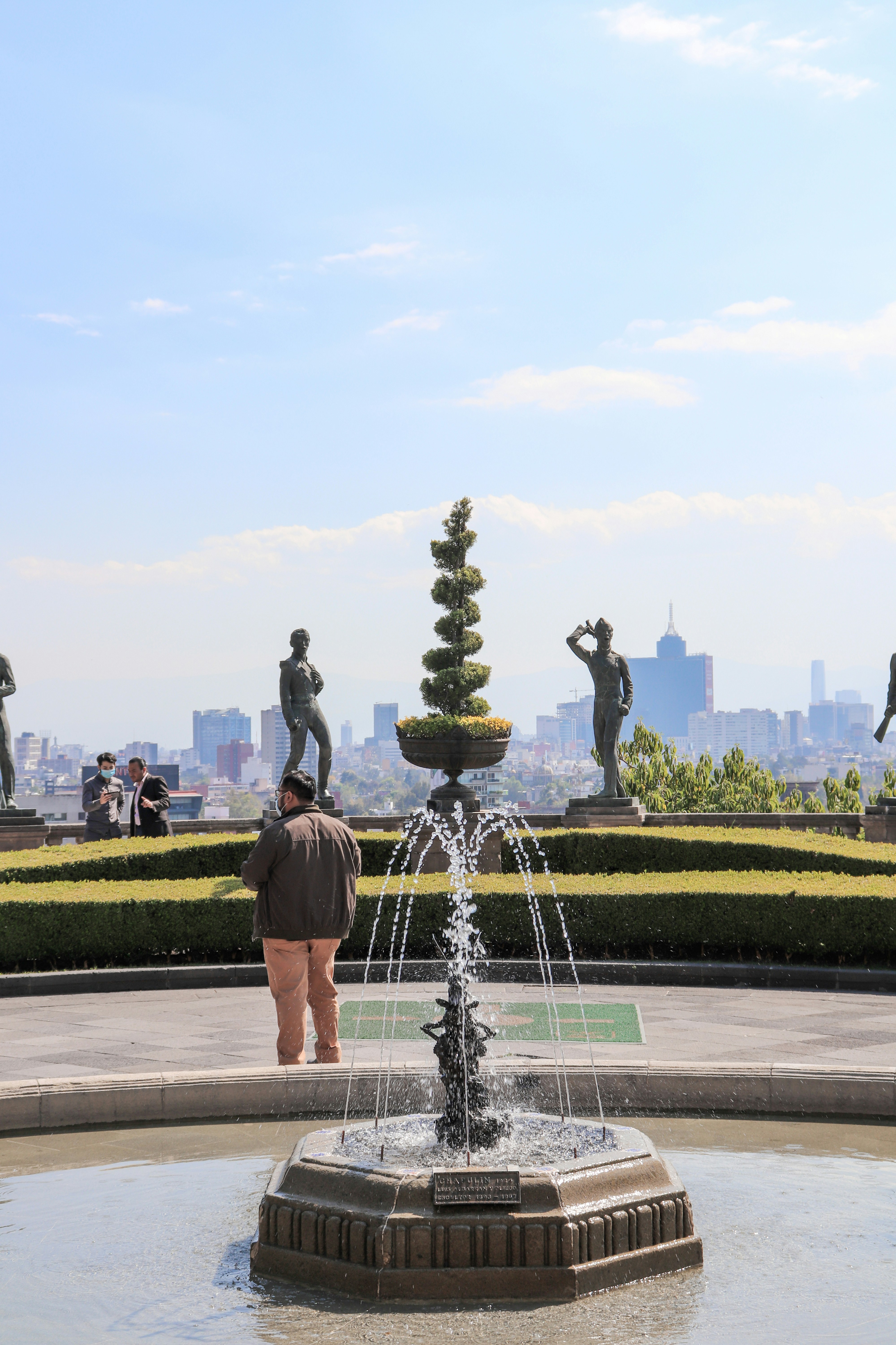 a man standing next to a fountain with statues in the background