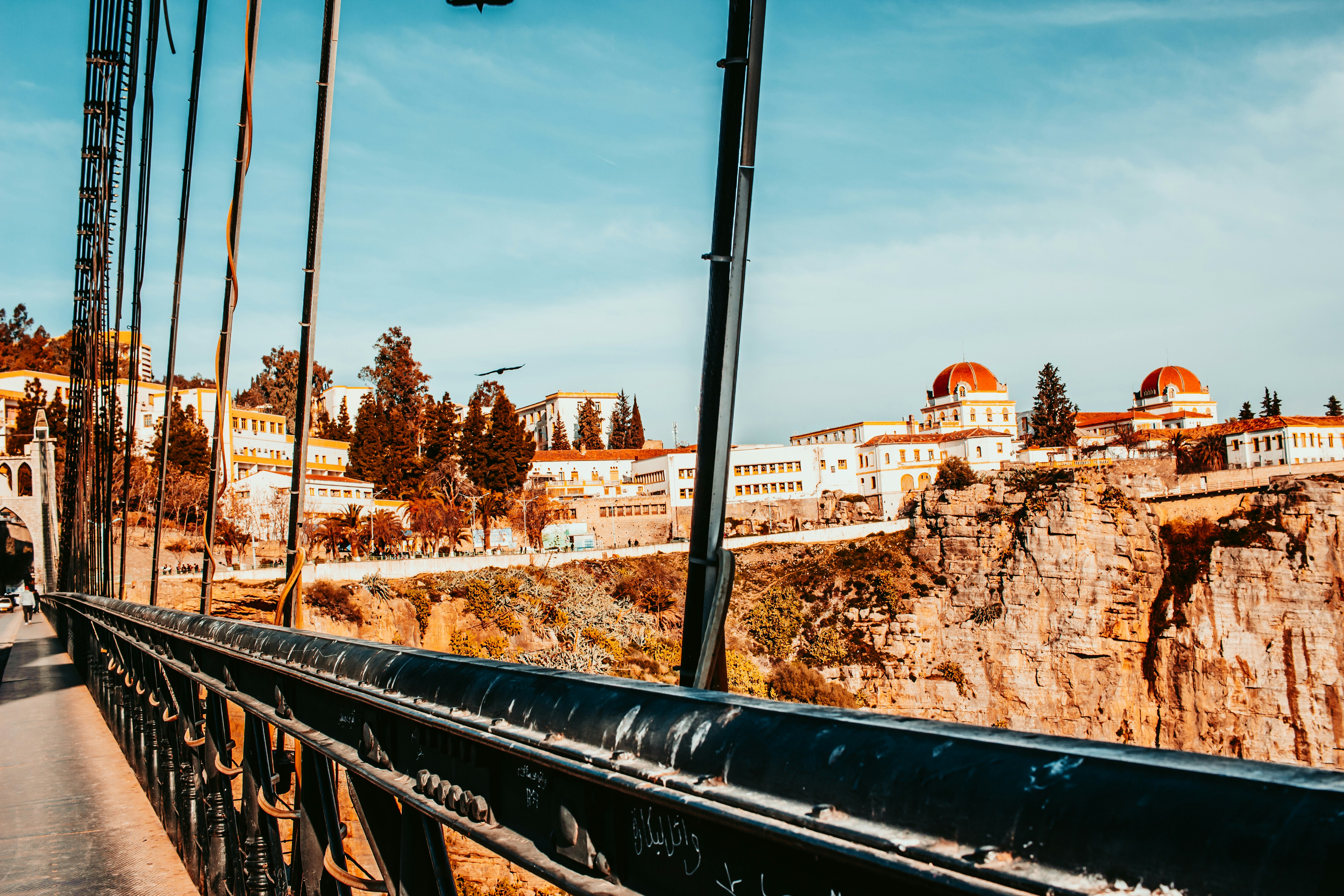 Suspension bridge leading to a cliffside town under a clear blue sky.