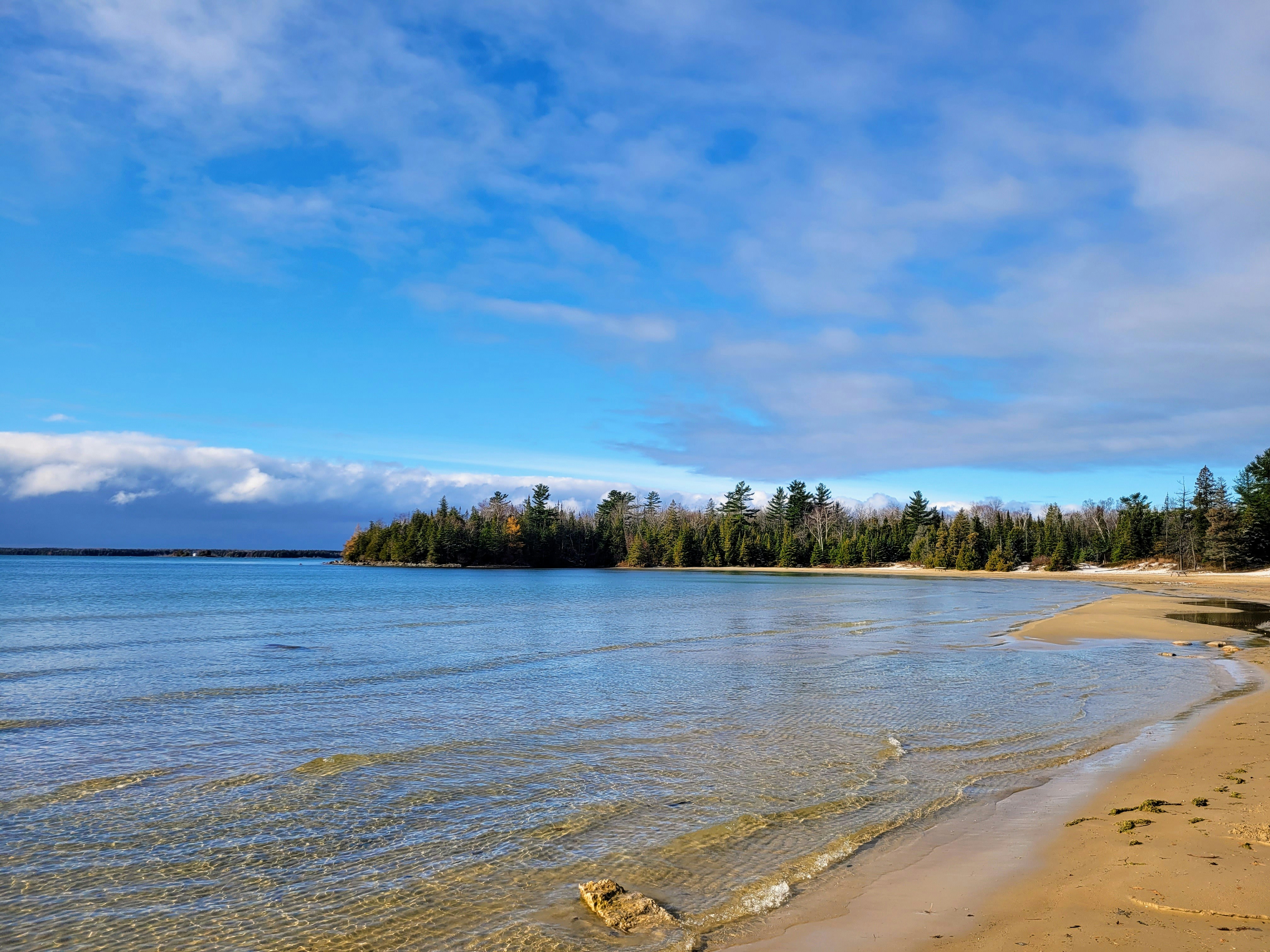 Sandy beach meeting calm waters under a wide expanse of blue sky with scattered clouds.