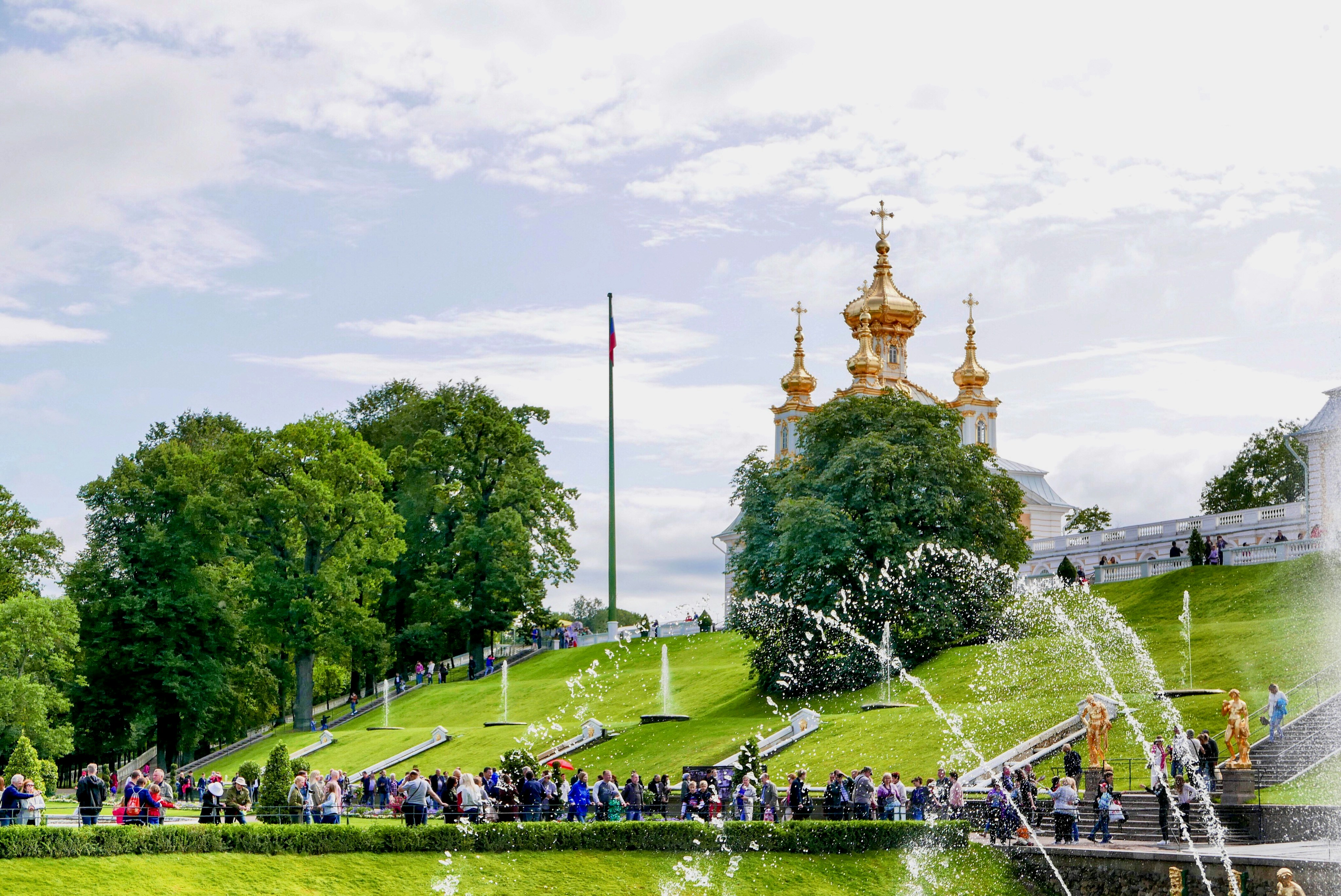 Crowd gathered around a fountain with ornate golden spires in the background.