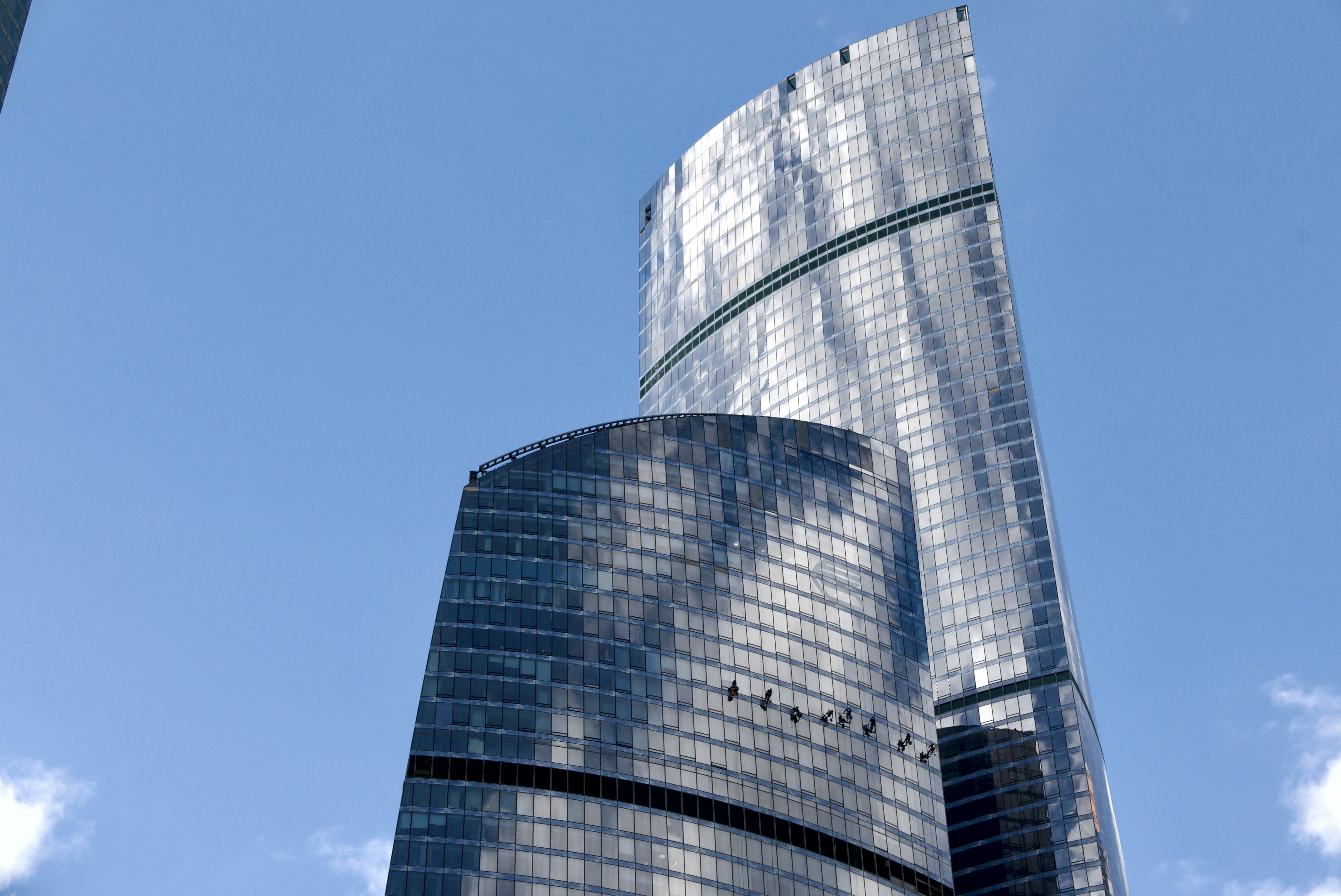 Reflection-rich glass towers twist upward against a clear blue sky, emphasizing curved façades and modern geometry. This architectural photograph highlights the towers' sweeping curves and metallic skin.