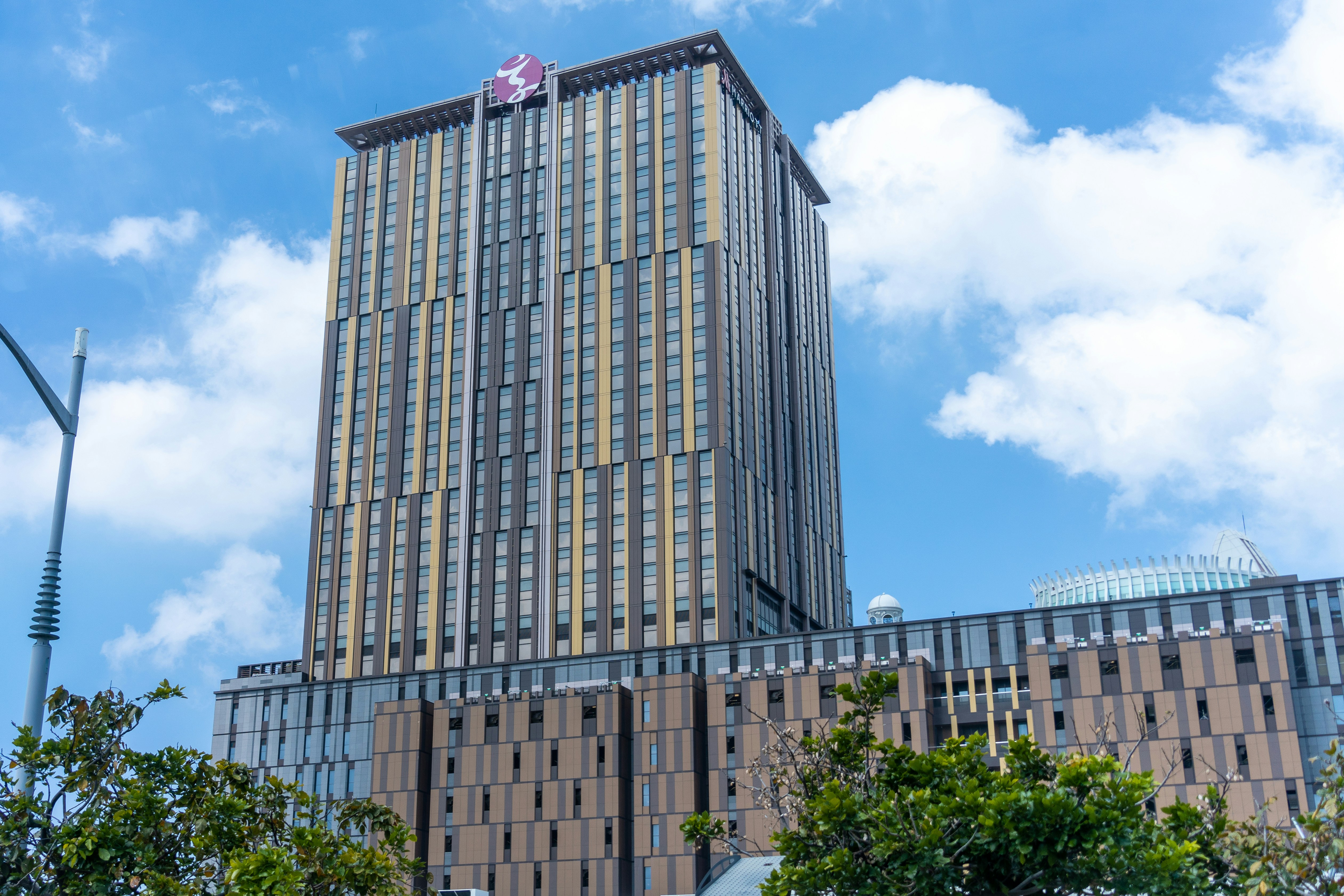 Modern skyscraper with a flag atop, set against a backdrop of vibrant clouds and a clear sky.