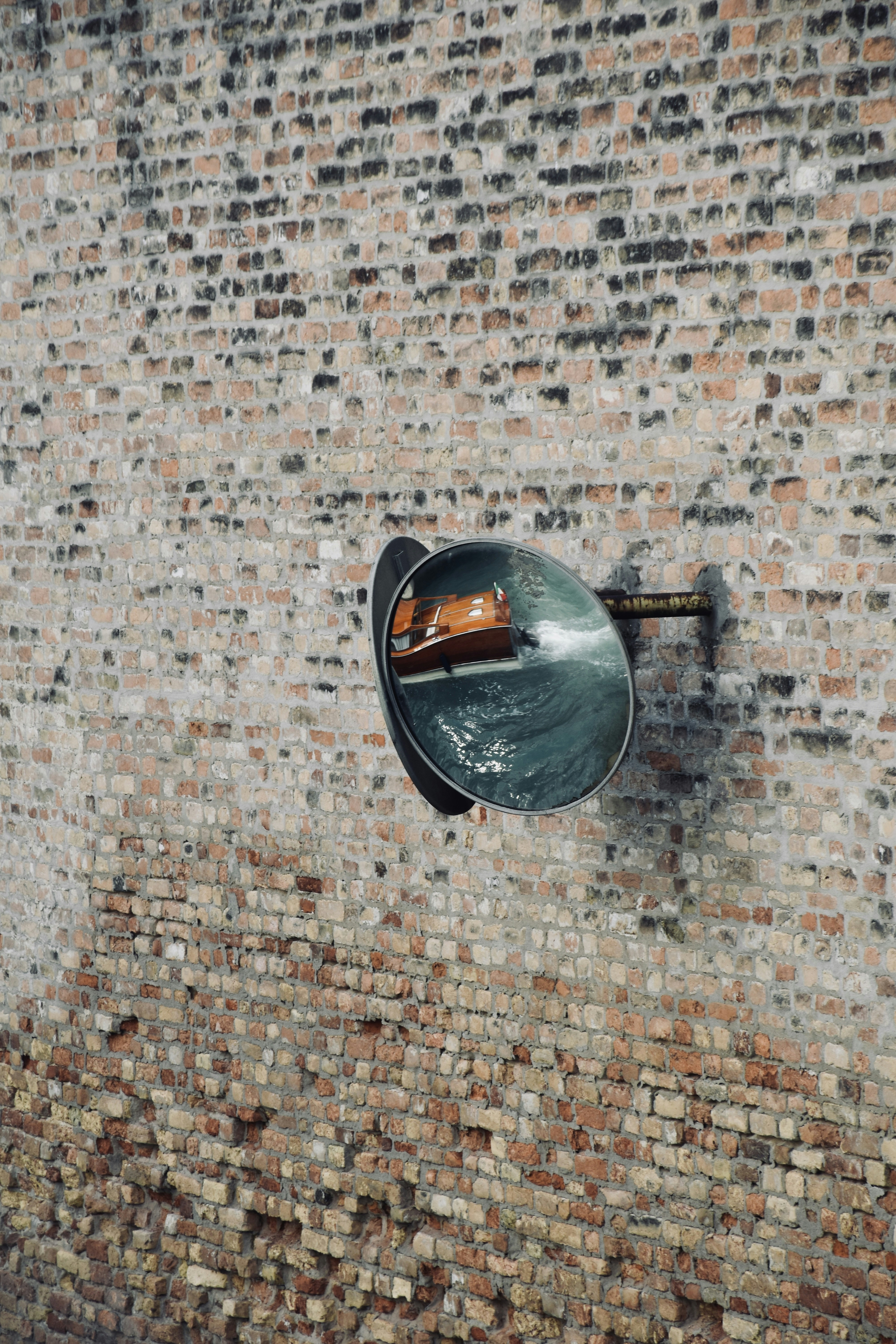 Circular Mirror on Brick Wall Reflects a Wooden Boat on Rippling Water