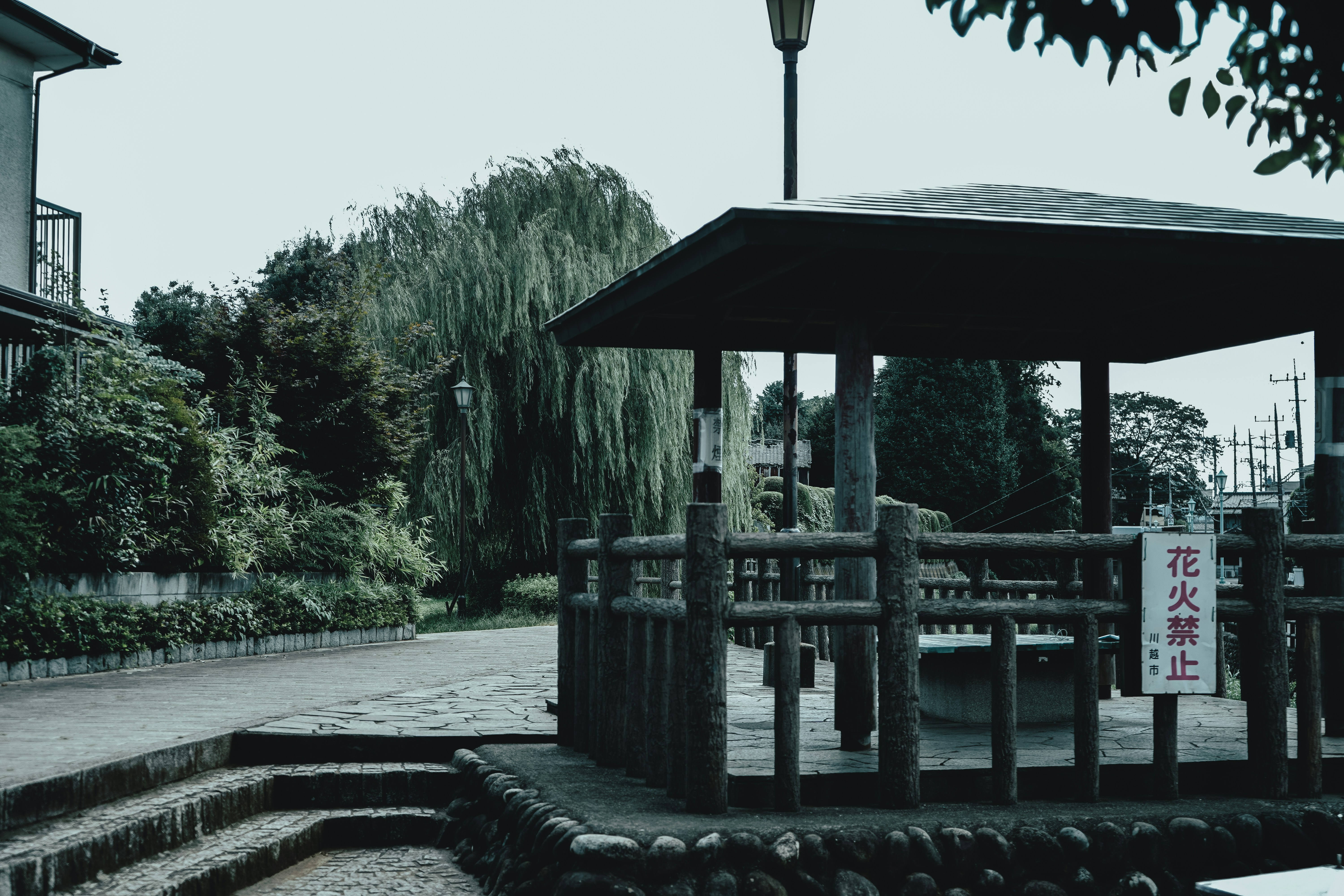 Wooden pavilion surrounded by lush foliage and a misty atmosphere, evoking tranquility.