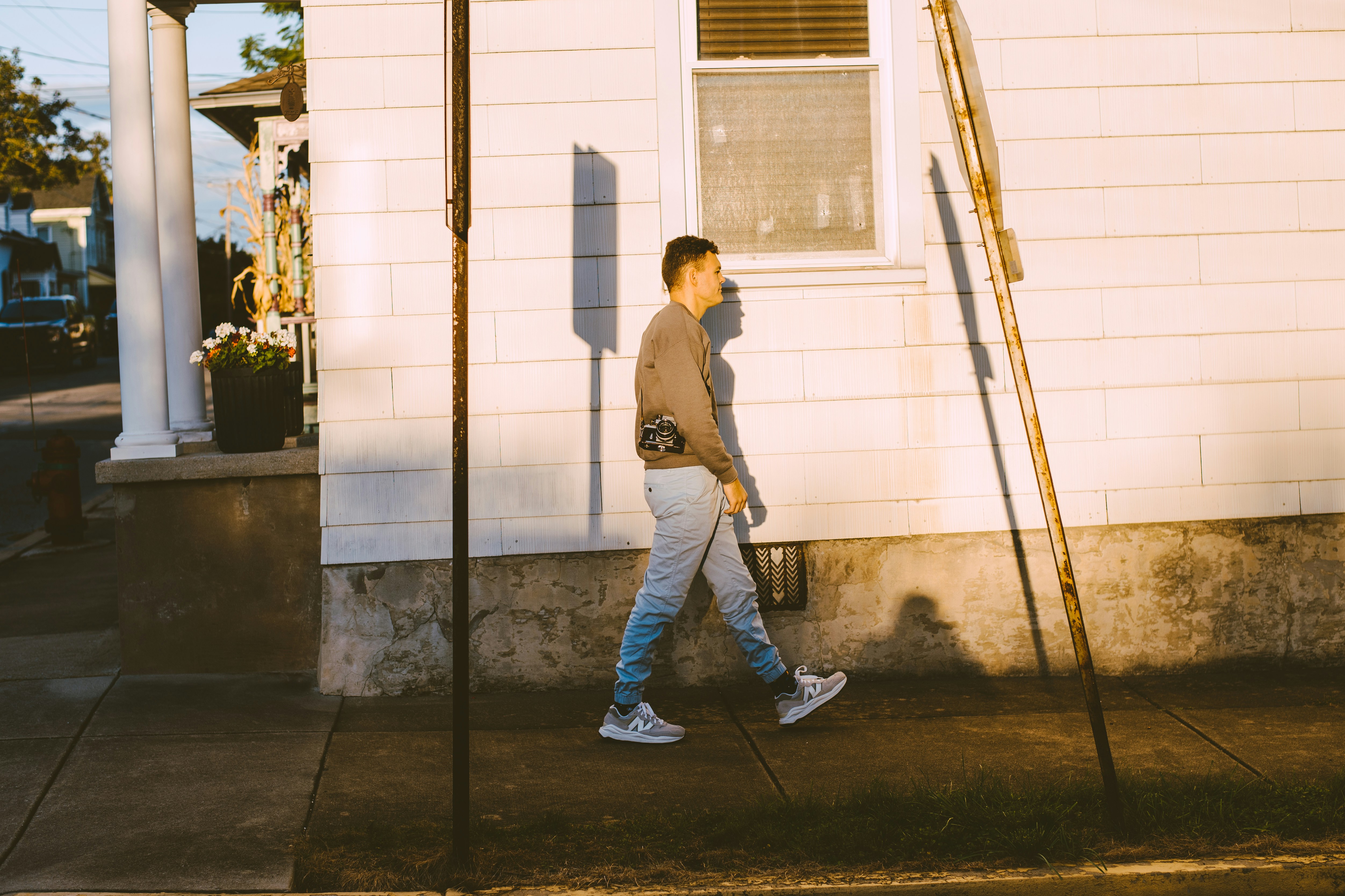 Sunlit stride along a pale facade: a lone walker in a quiet street