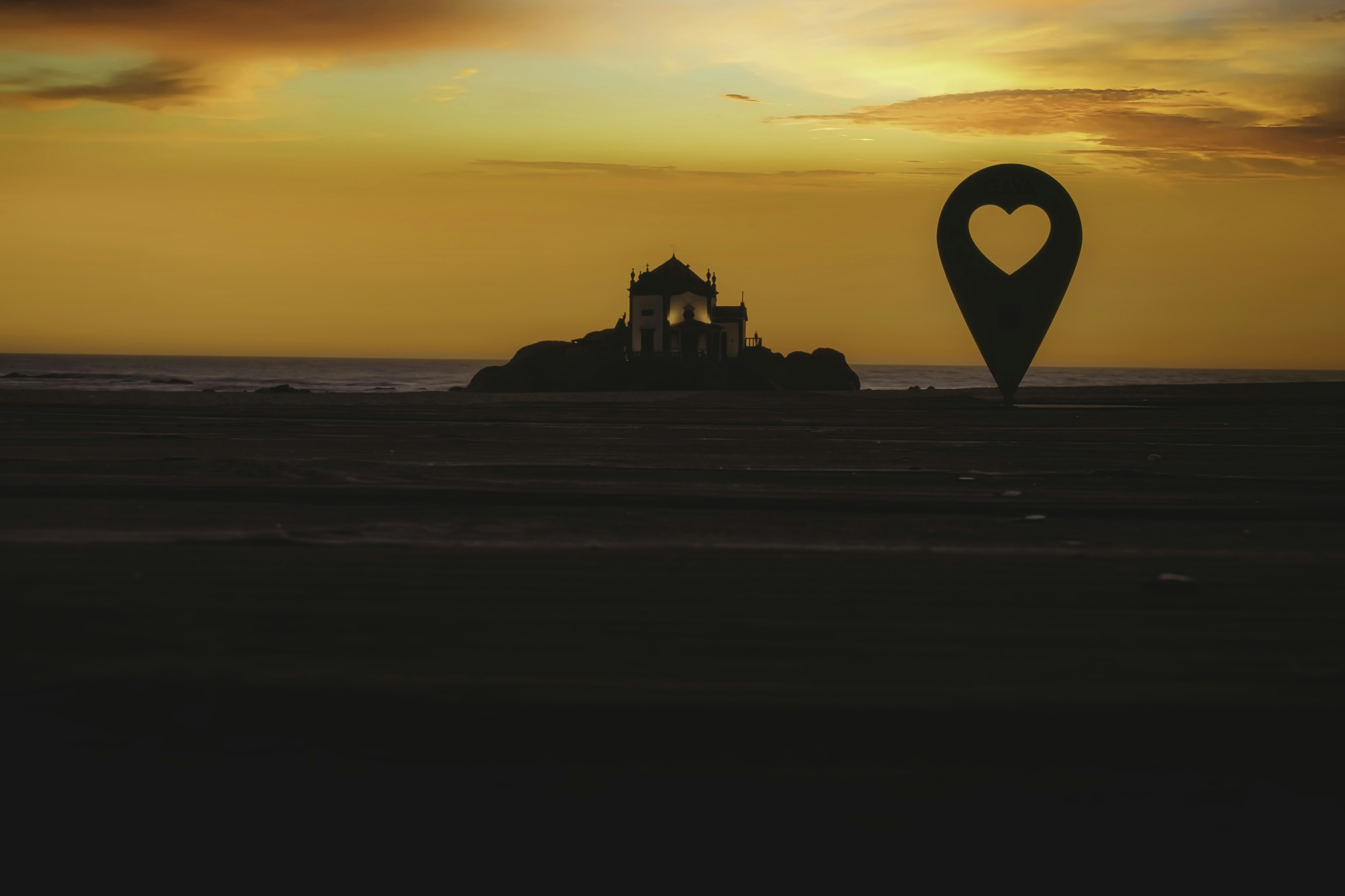 Silhouette of a small building and heart-shaped marker against a vibrant sunset sky.