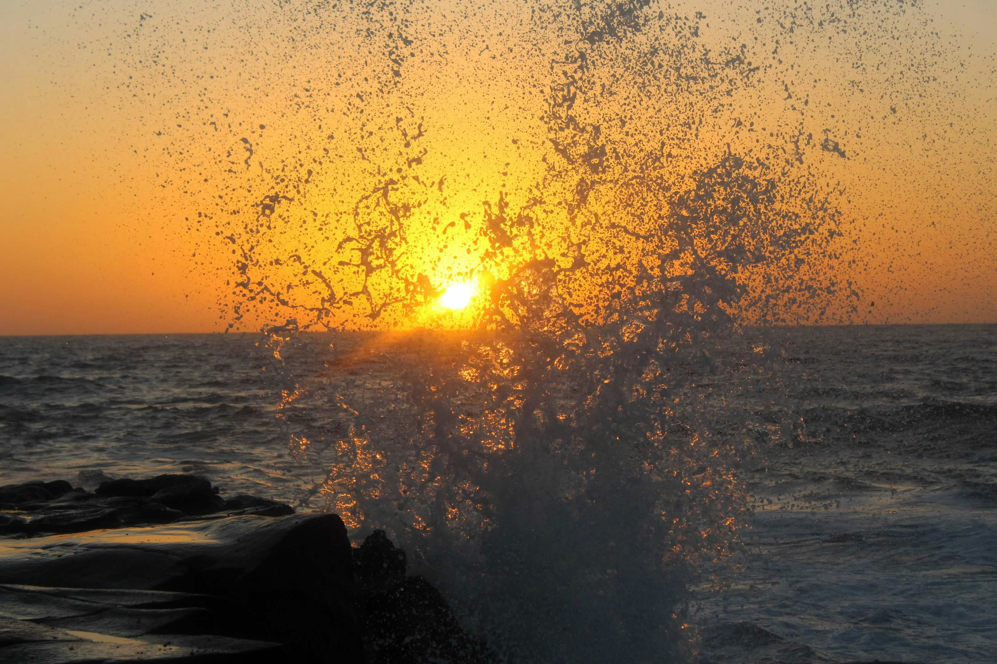 Ocean waves crashing against rocks as the sun sets, creating a misty spray in the golden light.