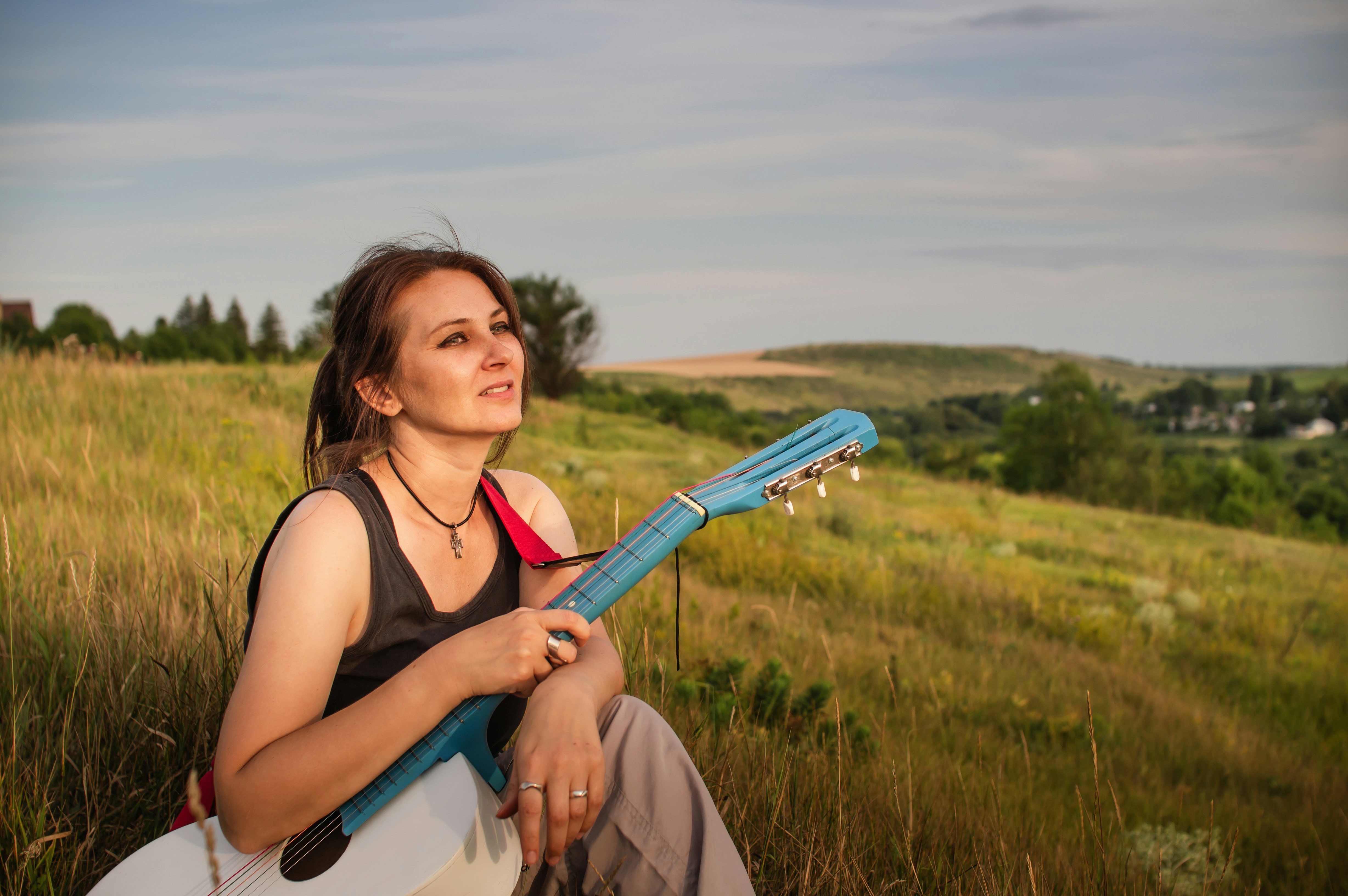 Sunlit Serenade: A Woman with a Blue Guitar in a Rolling Meadow