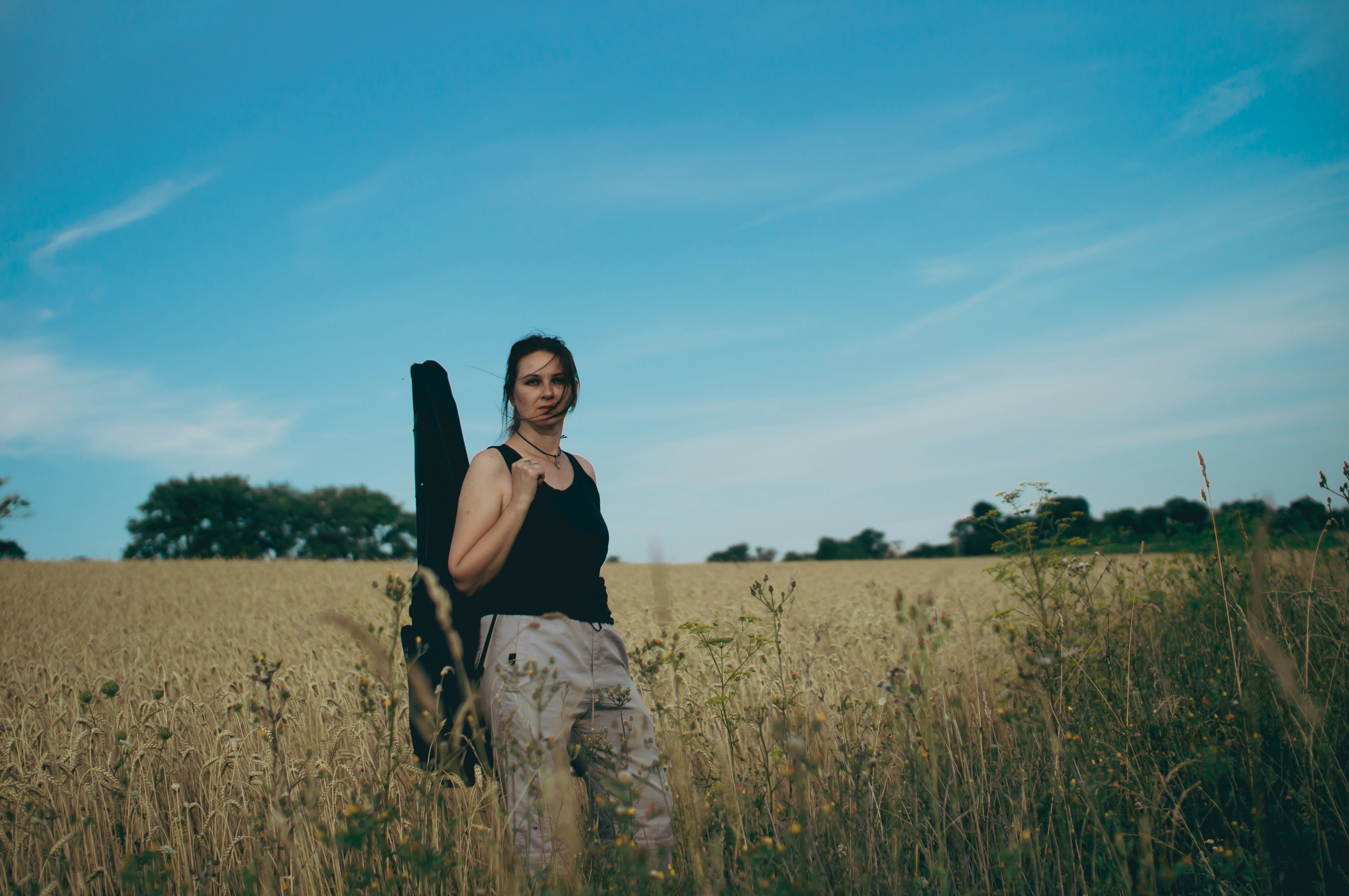 Golden Field Portrait: A Woman with a Guitar Case Beneath a Wide Blue Sky