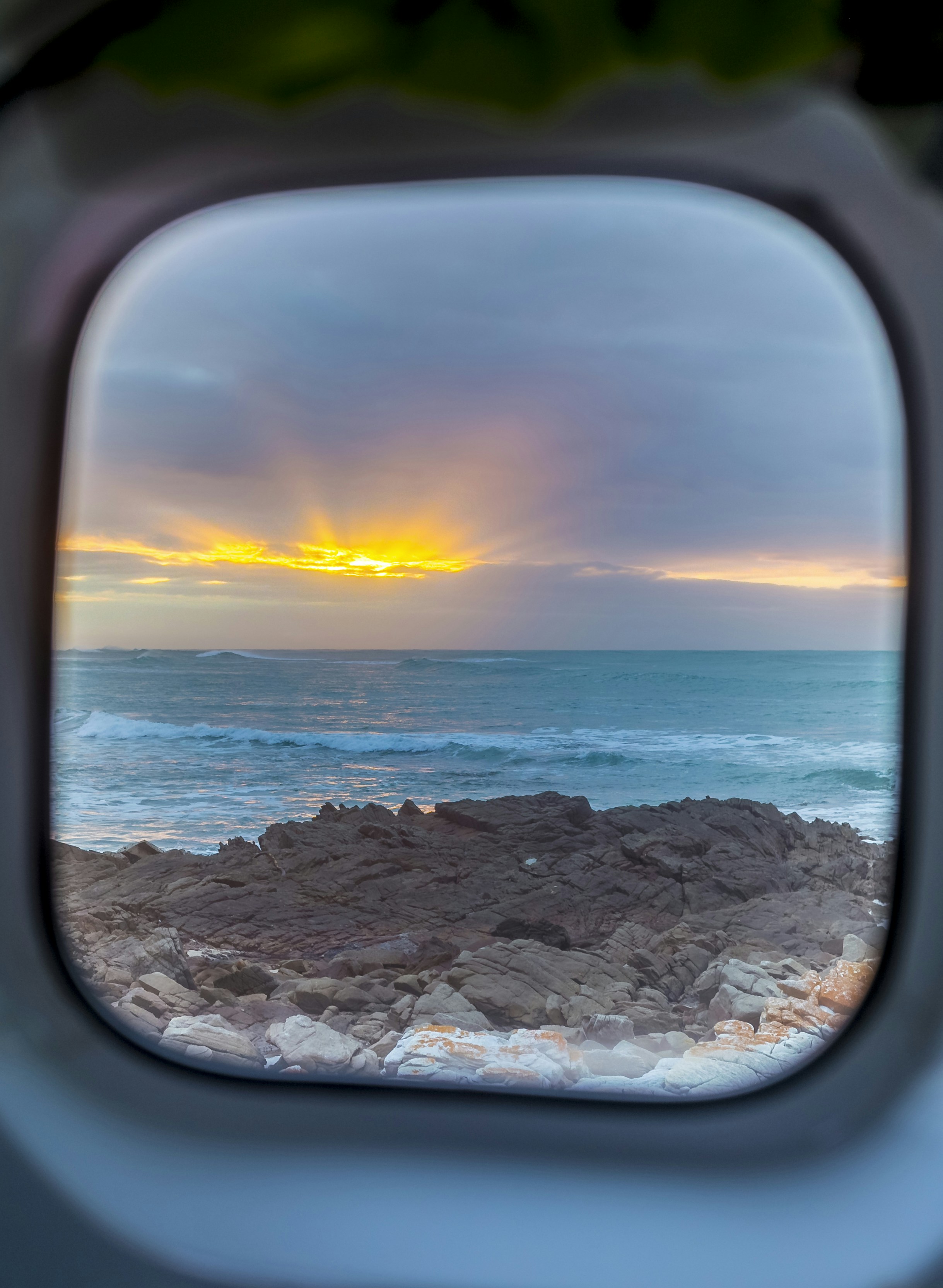 Golden Horizon Framed by a Rocky Coast, Seen Through an Airplane Window