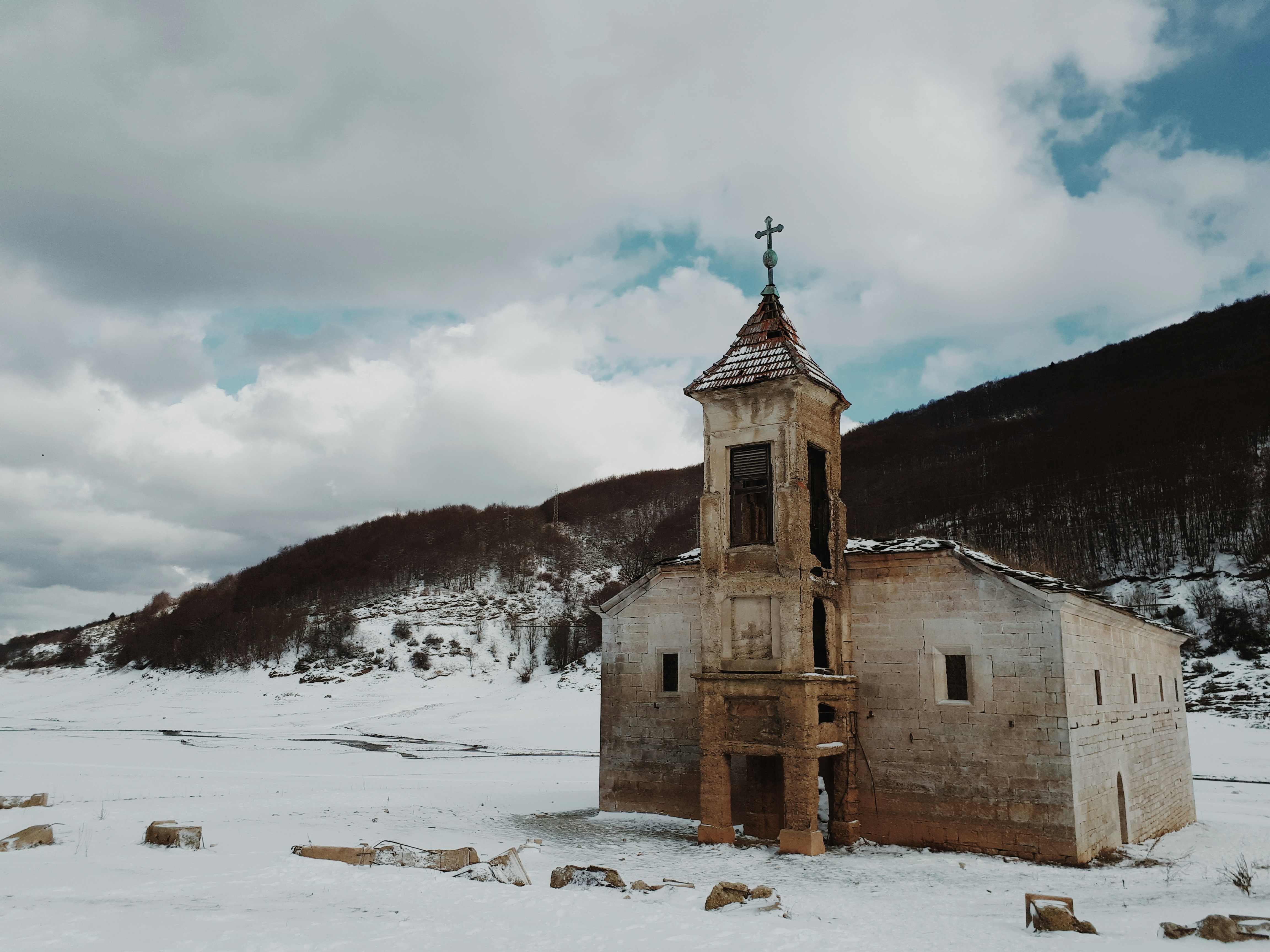 Abandoned church rising from a snowy landscape, surrounded by a serene lake and distant hills. The structure's weathered facade tells a story of time and nature's embrace.