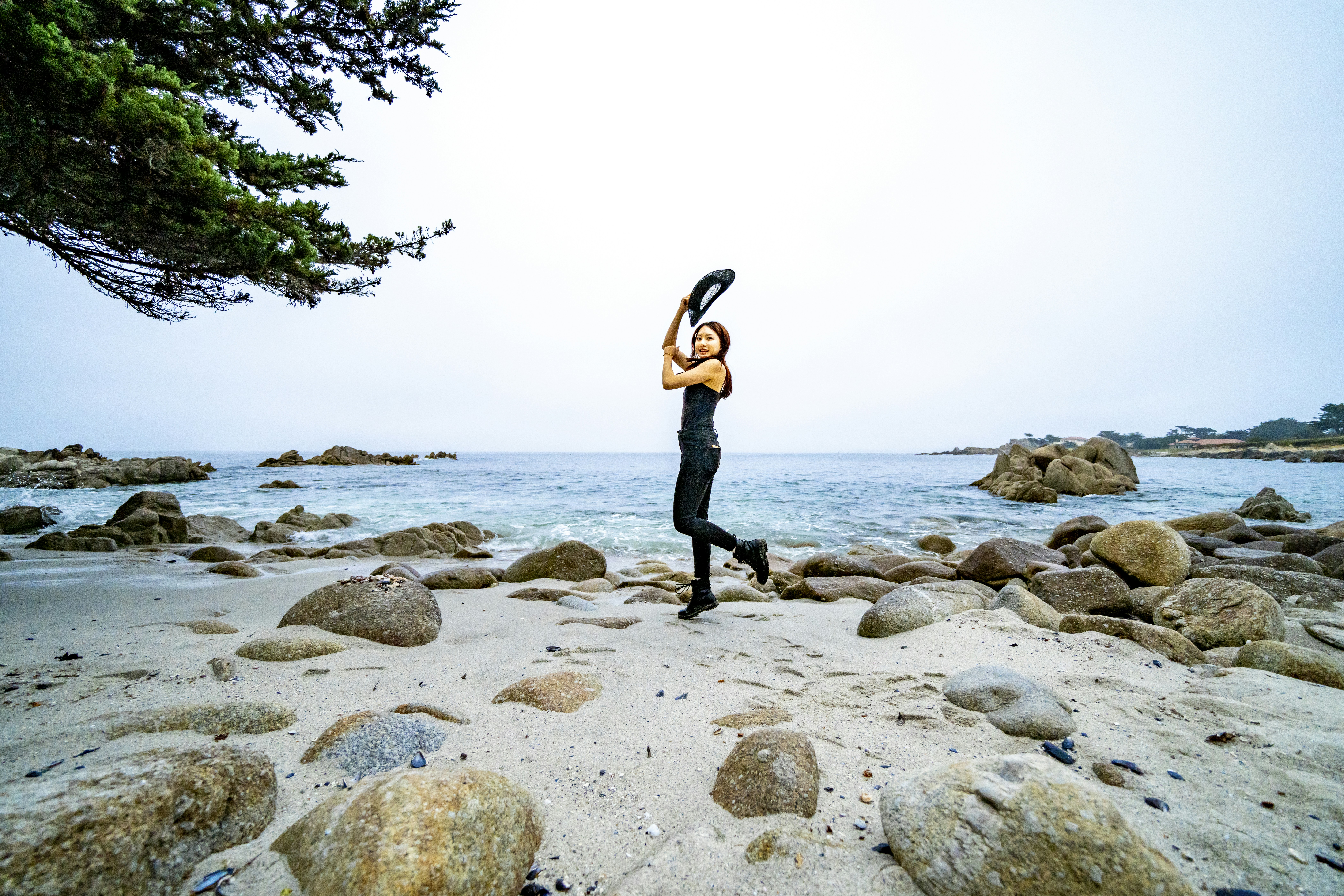 Portrait of a young woman jumping on a rocky California beach with a cowboy hat in hand