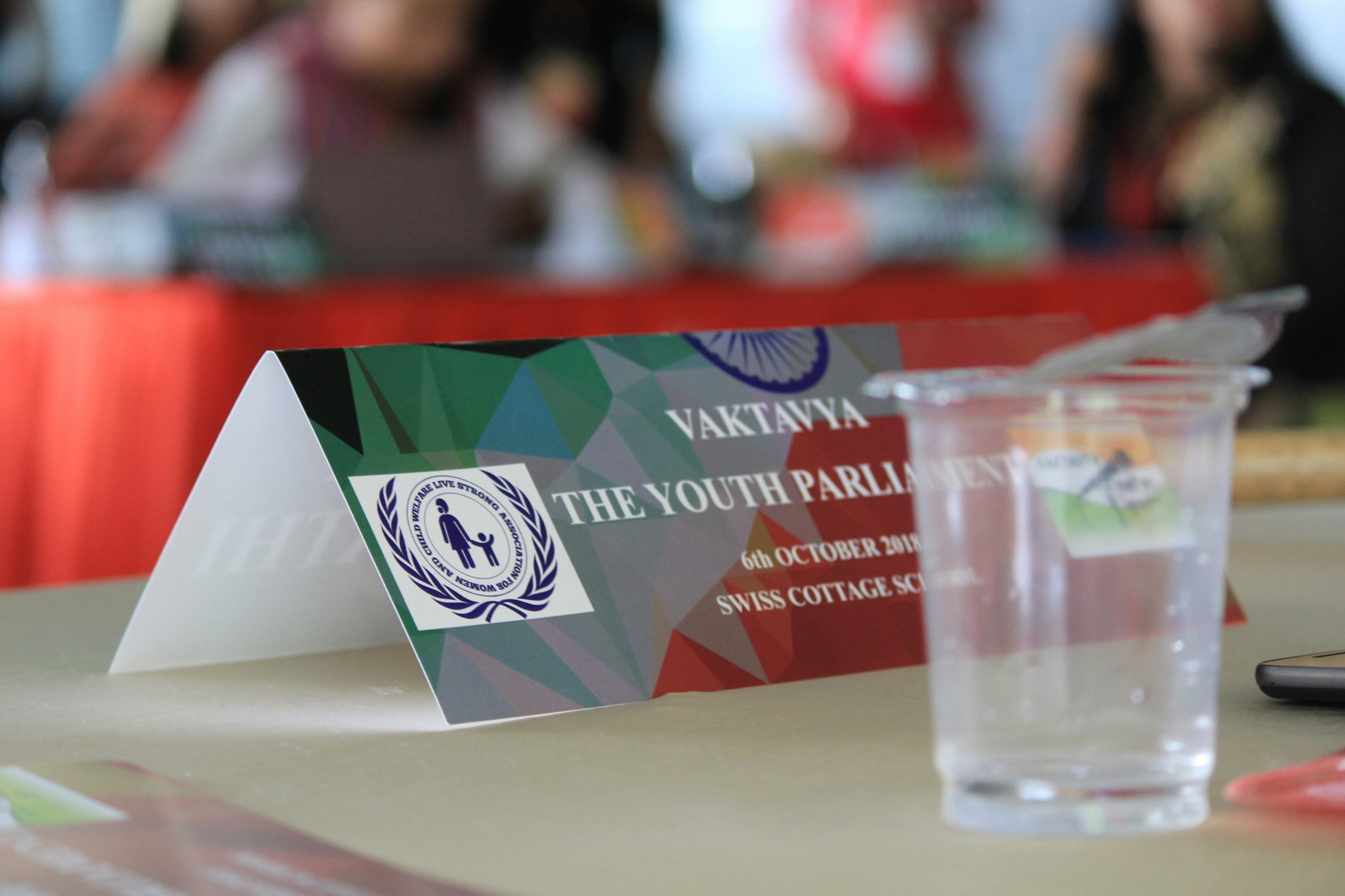 A triangular table sign for 'Vaktawia: The Youth Parliament' displayed prominently on a table amidst a blurred background of attendees.
