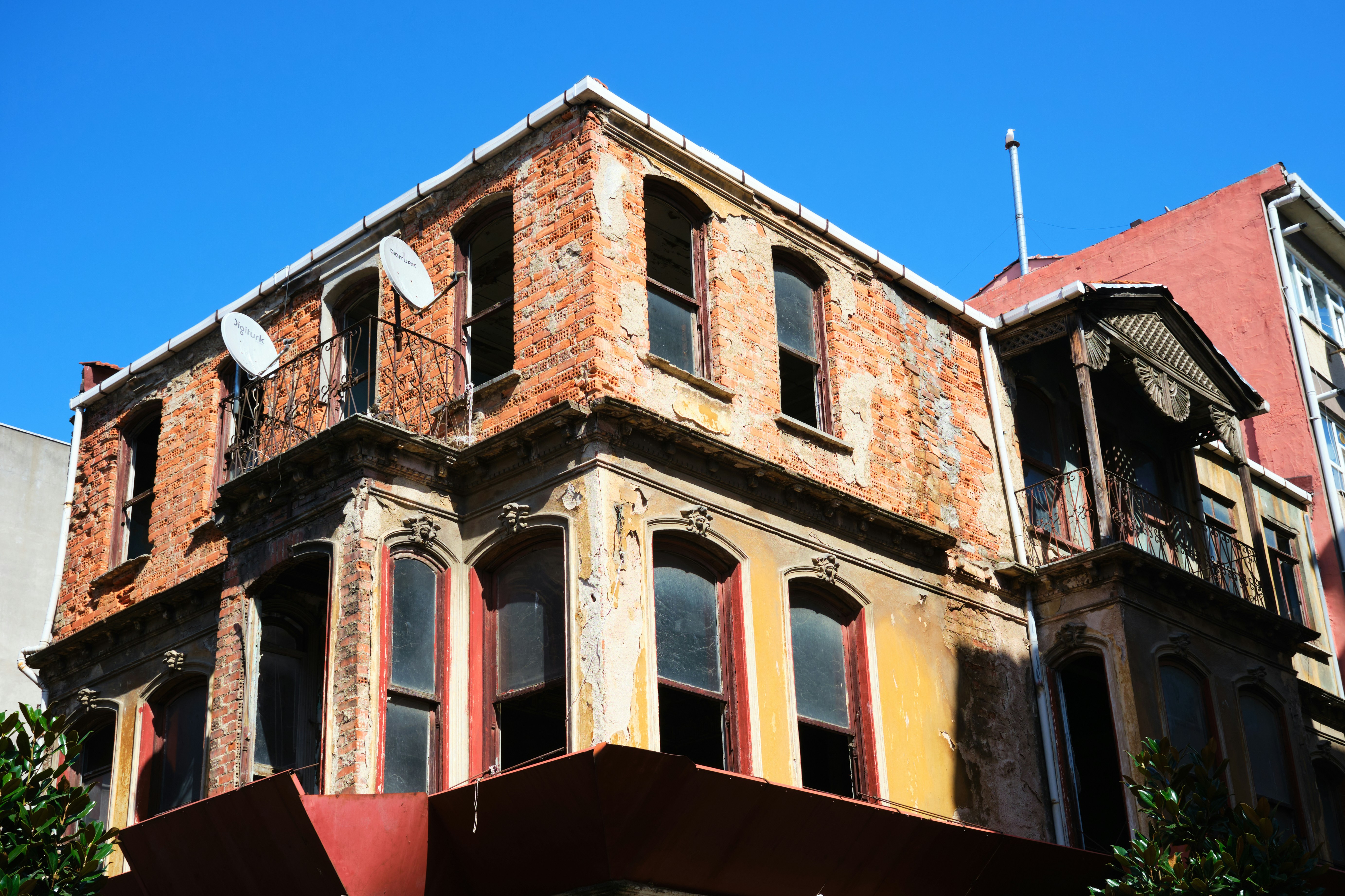 Corner Facade in Sunlight: Weathered Brick, Red Arches, and a Narrow Awning