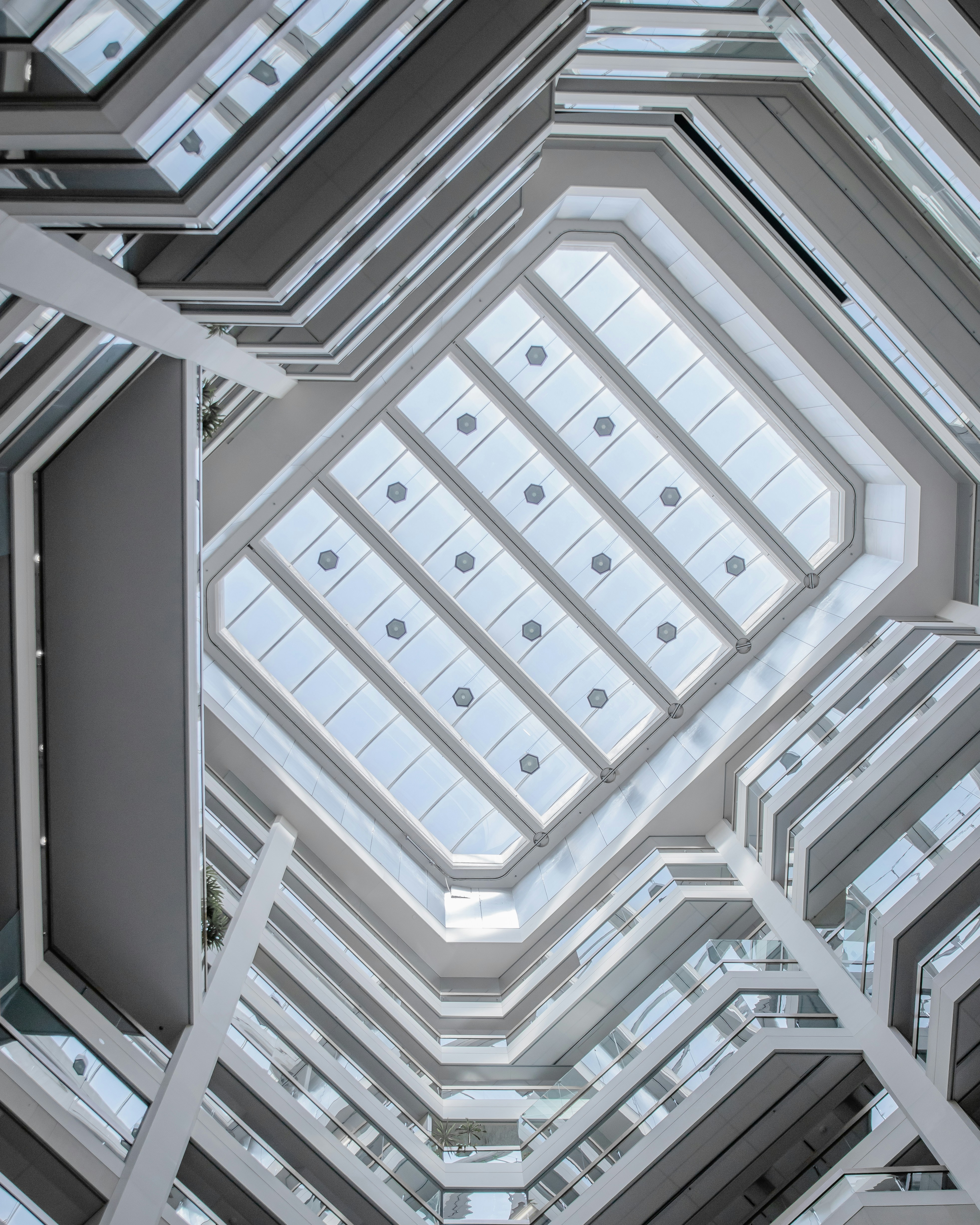 Interior view of a modern building showcasing a geometric ceiling with large glass panels and angular lines. The design emphasizes light and space.