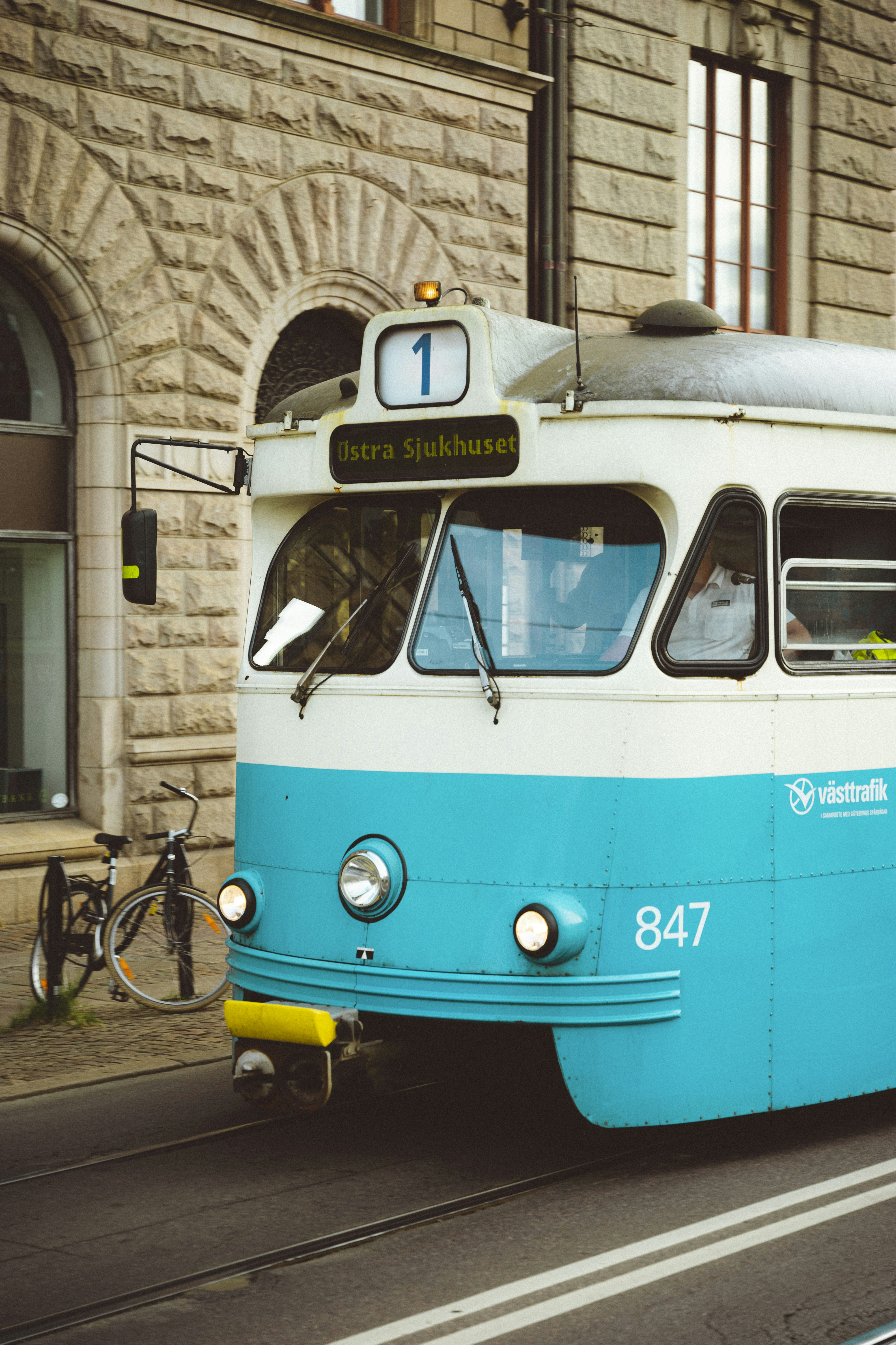 Blue tram at the curb: a vintage streetcar waiting by stone arches