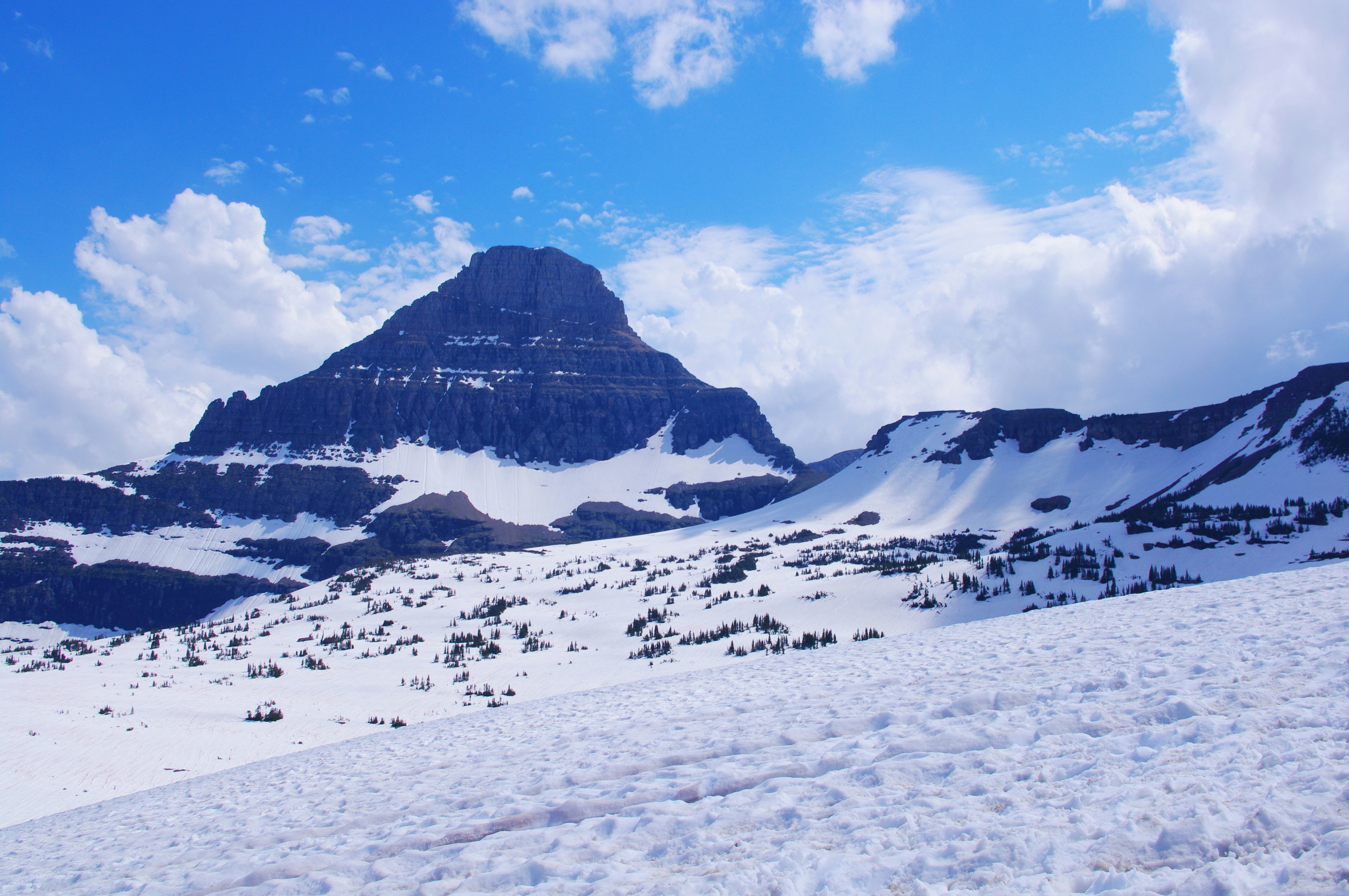 Snow-covered mountain peak under a bright blue sky with scattered clouds.