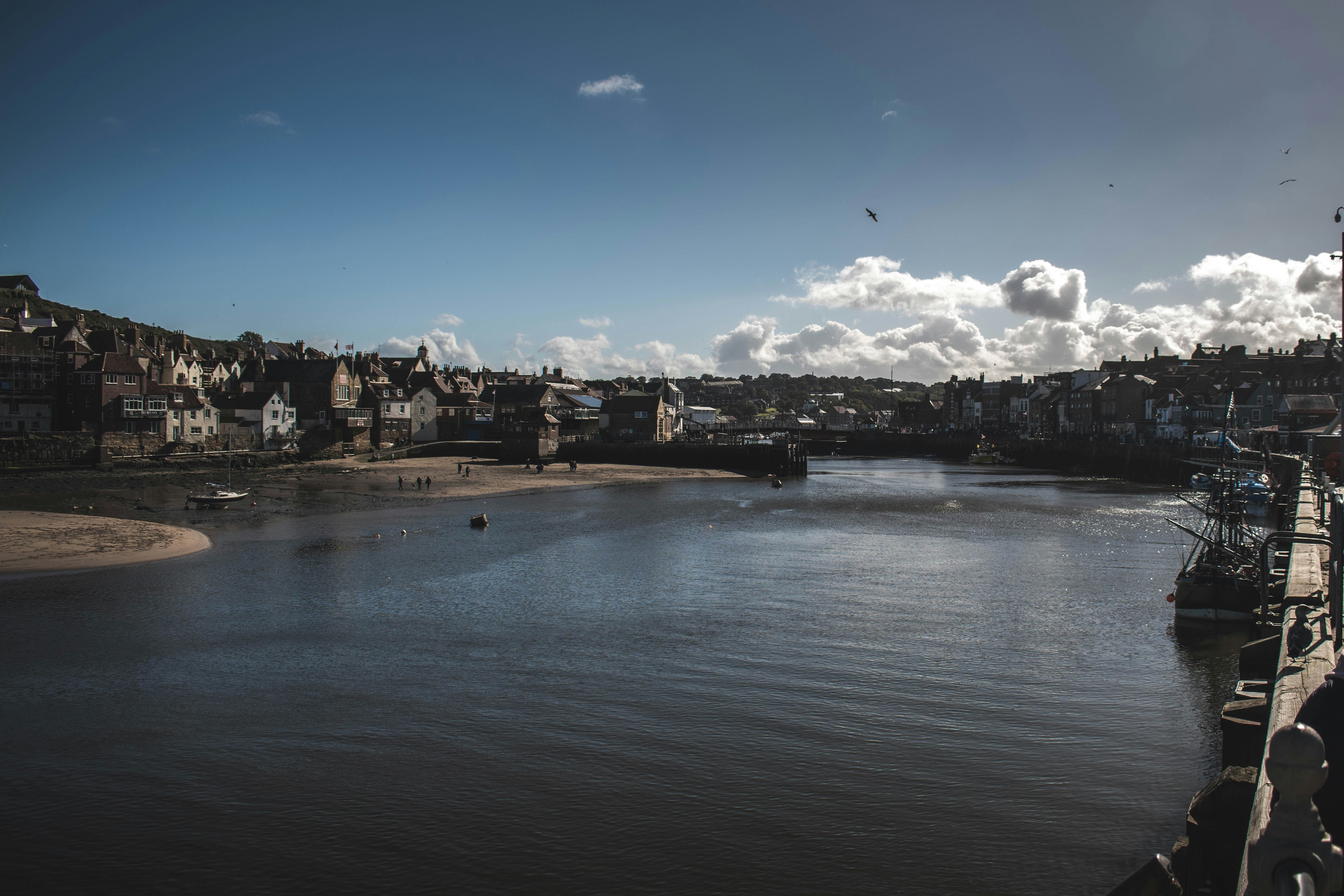 Quaint houses line the harbor, reflecting the tranquil waters under a partly cloudy sky. The scene captures a peaceful moment in a coastal town.