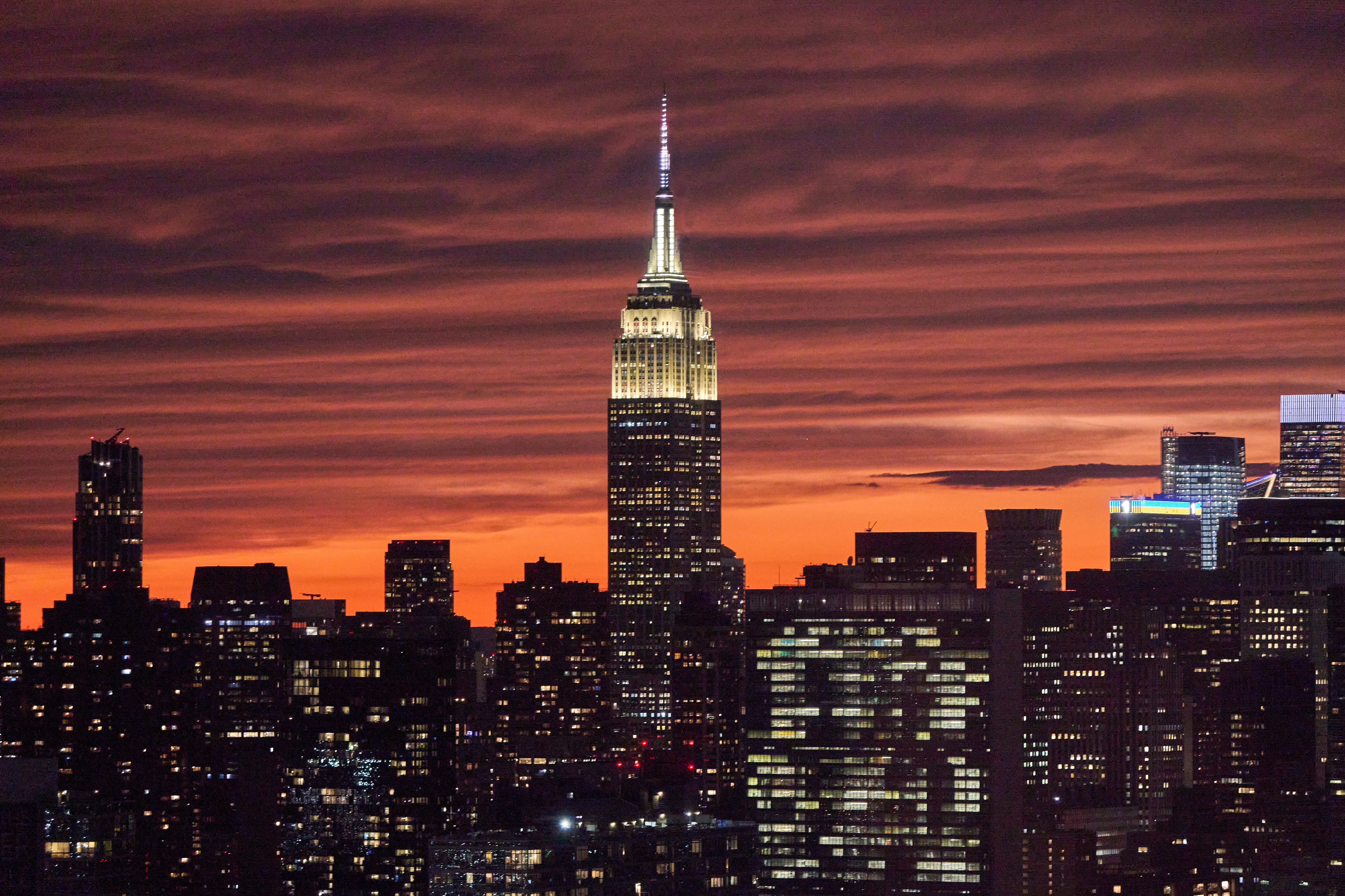 Empire State Building illuminated against a vibrant sunset sky with dramatic cloud patterns.