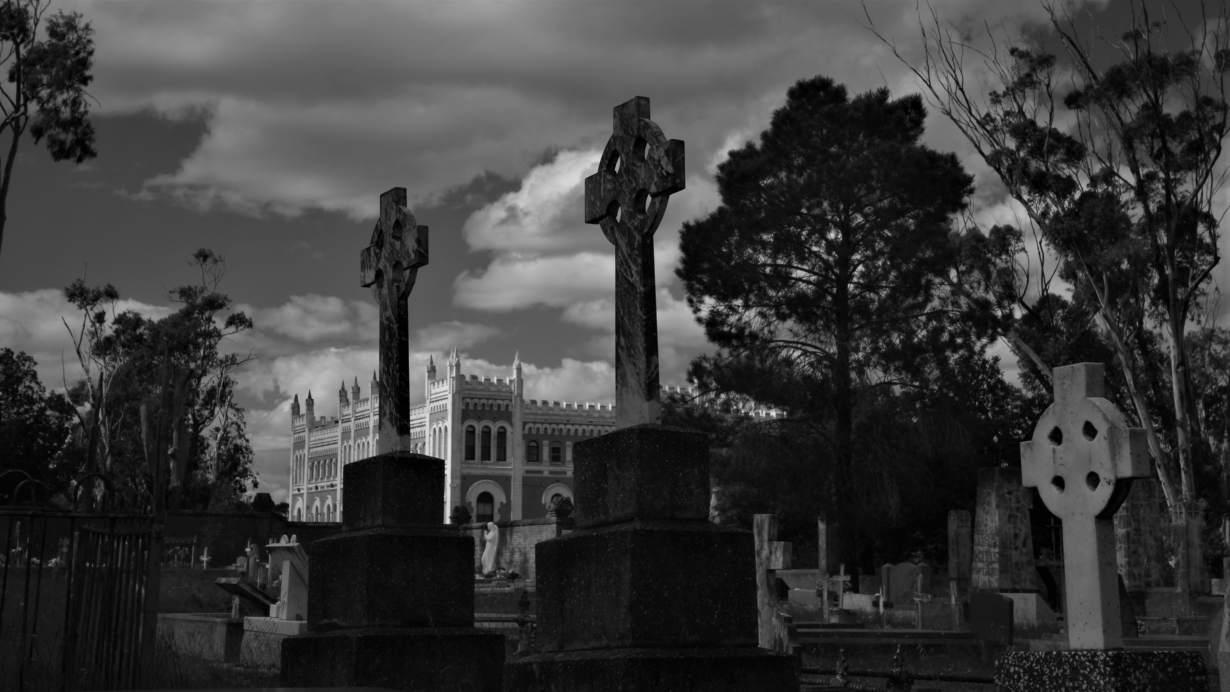 Celtic crosses stand solemnly in a cemetery, framed by a dramatic sky and distant architecture. The scene evokes a sense of history and reflection.