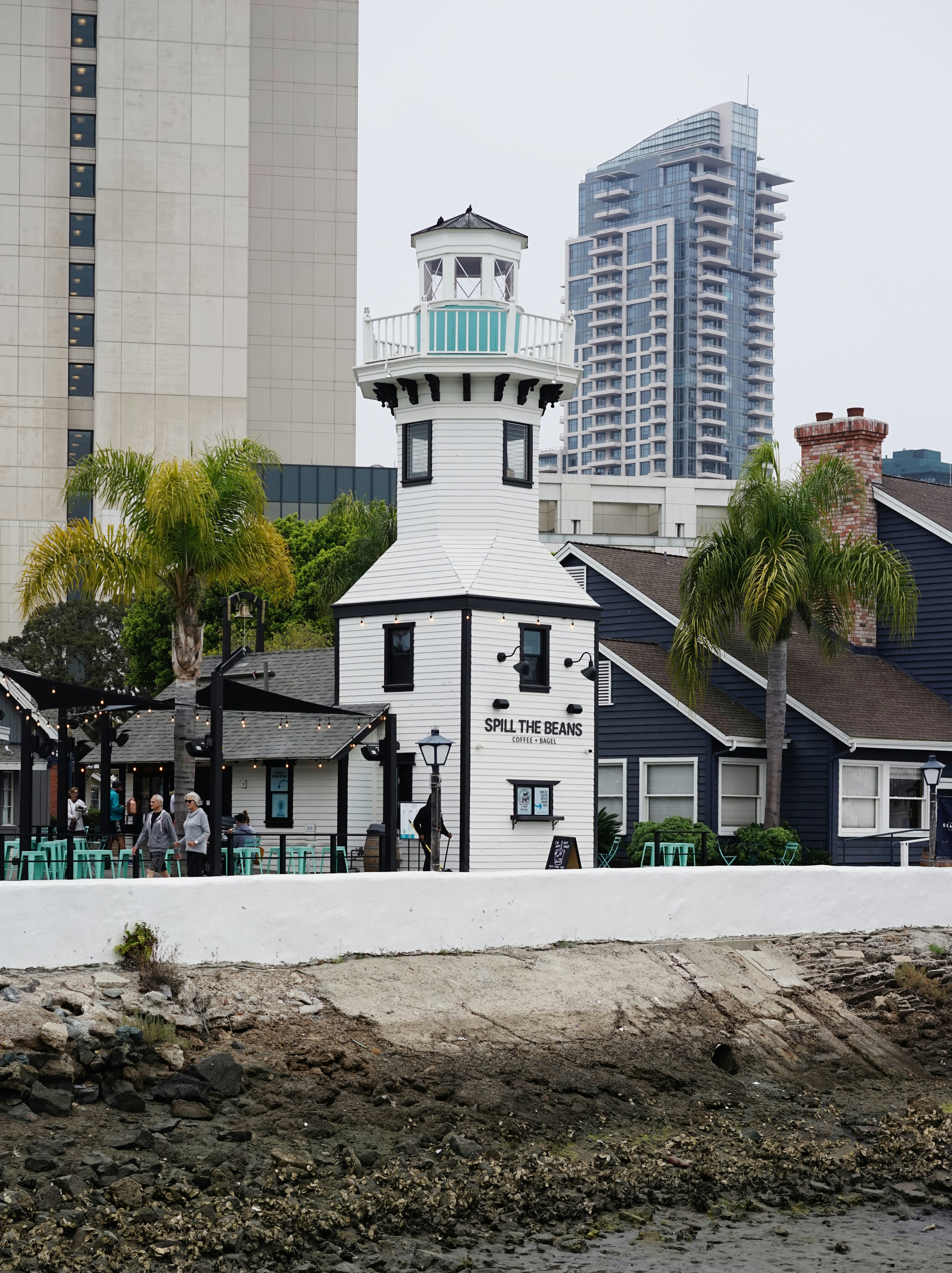Lighthouse at the Edge: Buildings, palms, and a weathered shoreline