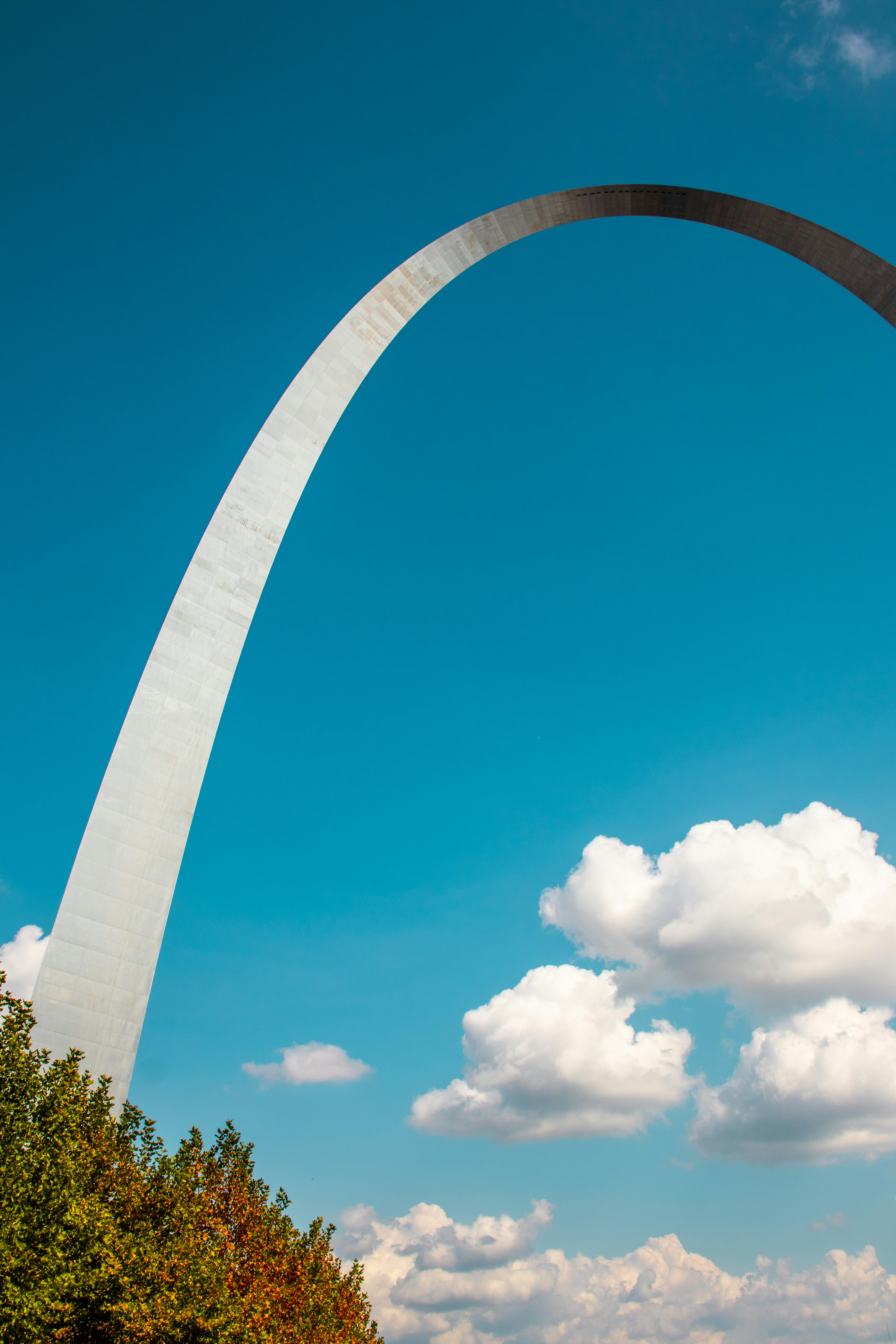 A large arch with trees in the background with Gateway Arch in the ...