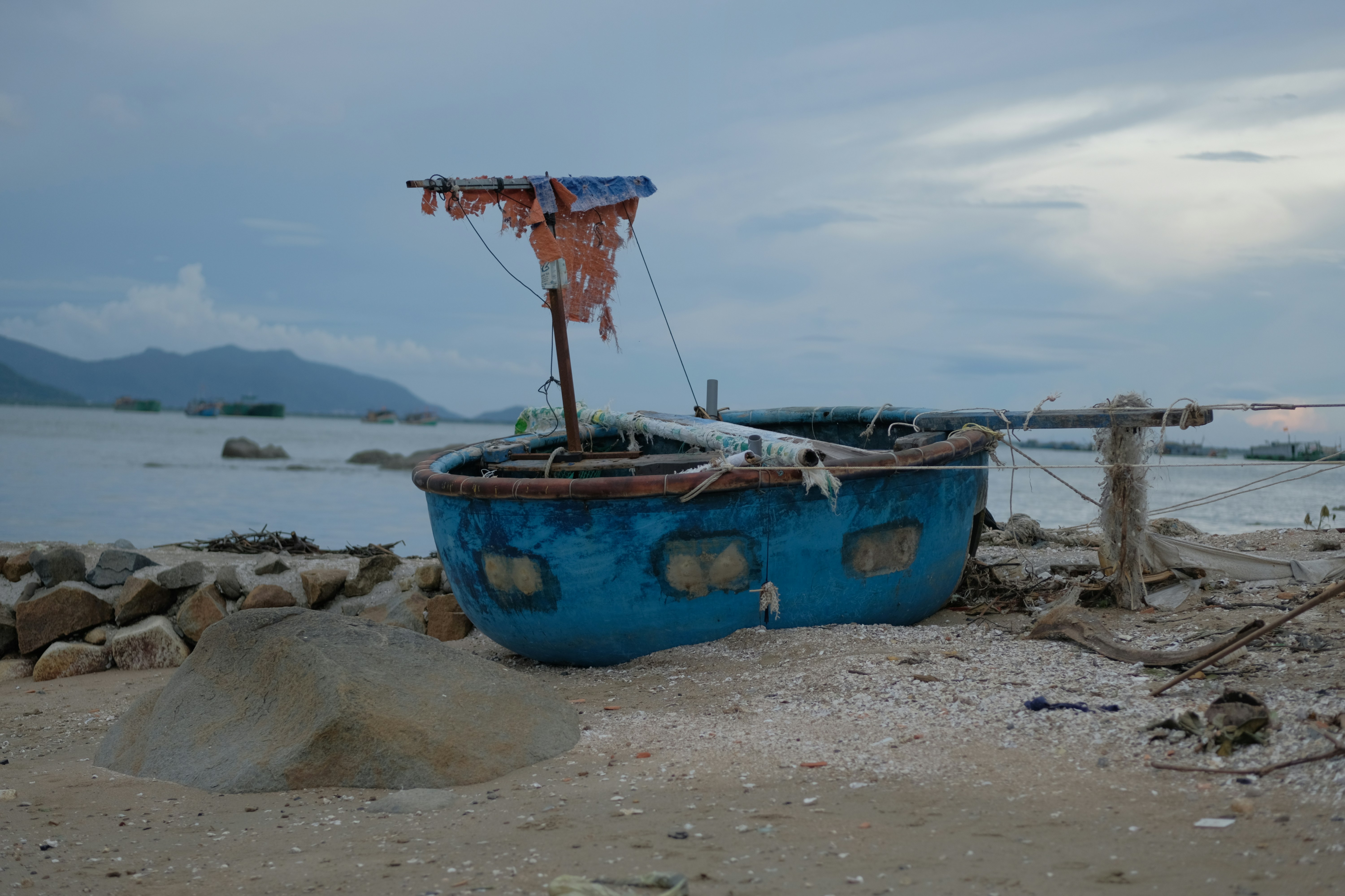 Weathered blue boat resting on a sandy beach with calm sea and cloudy sky in the background.
