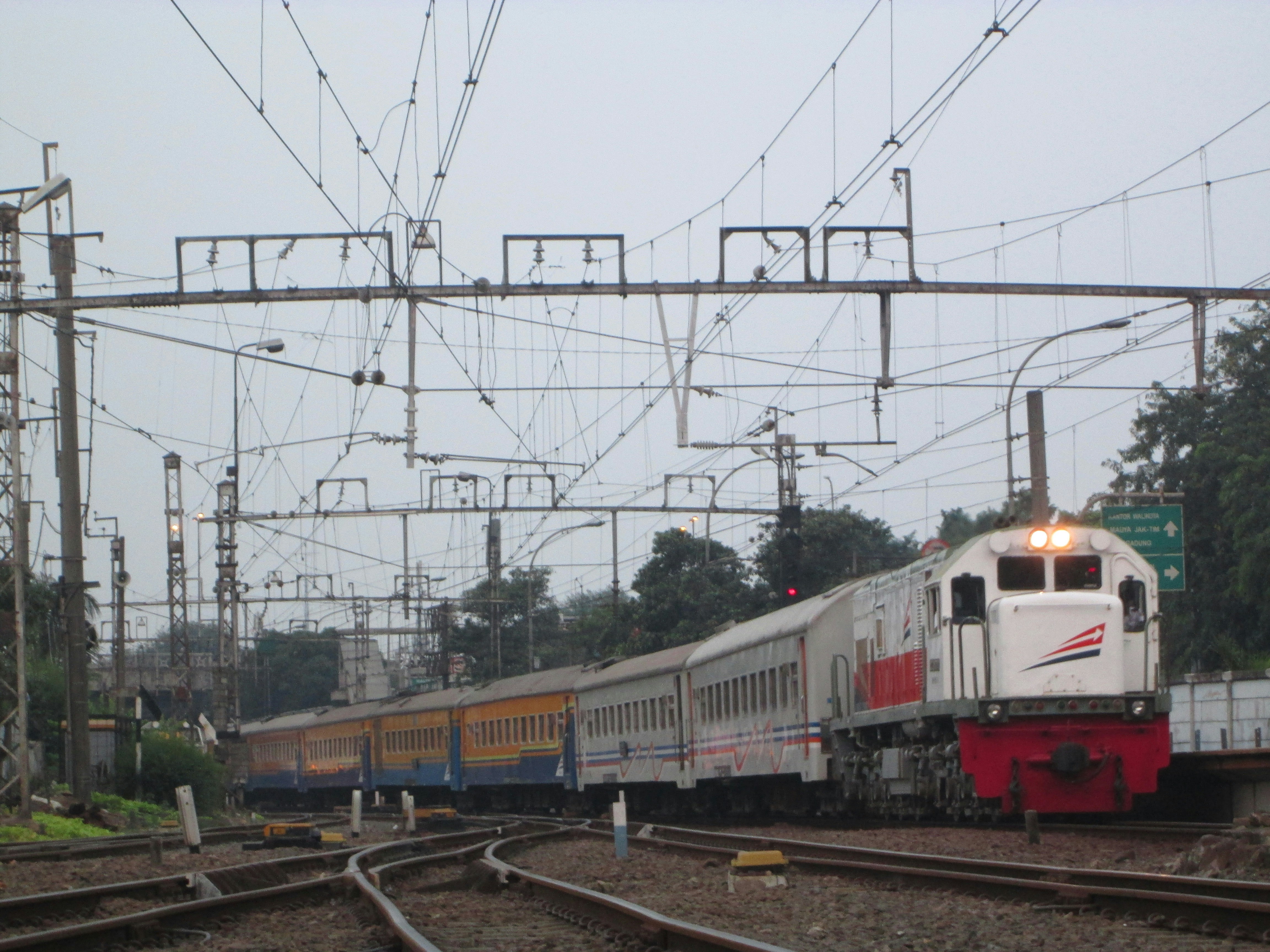 Train approaching Jatinegara Station under a network of overhead wires.