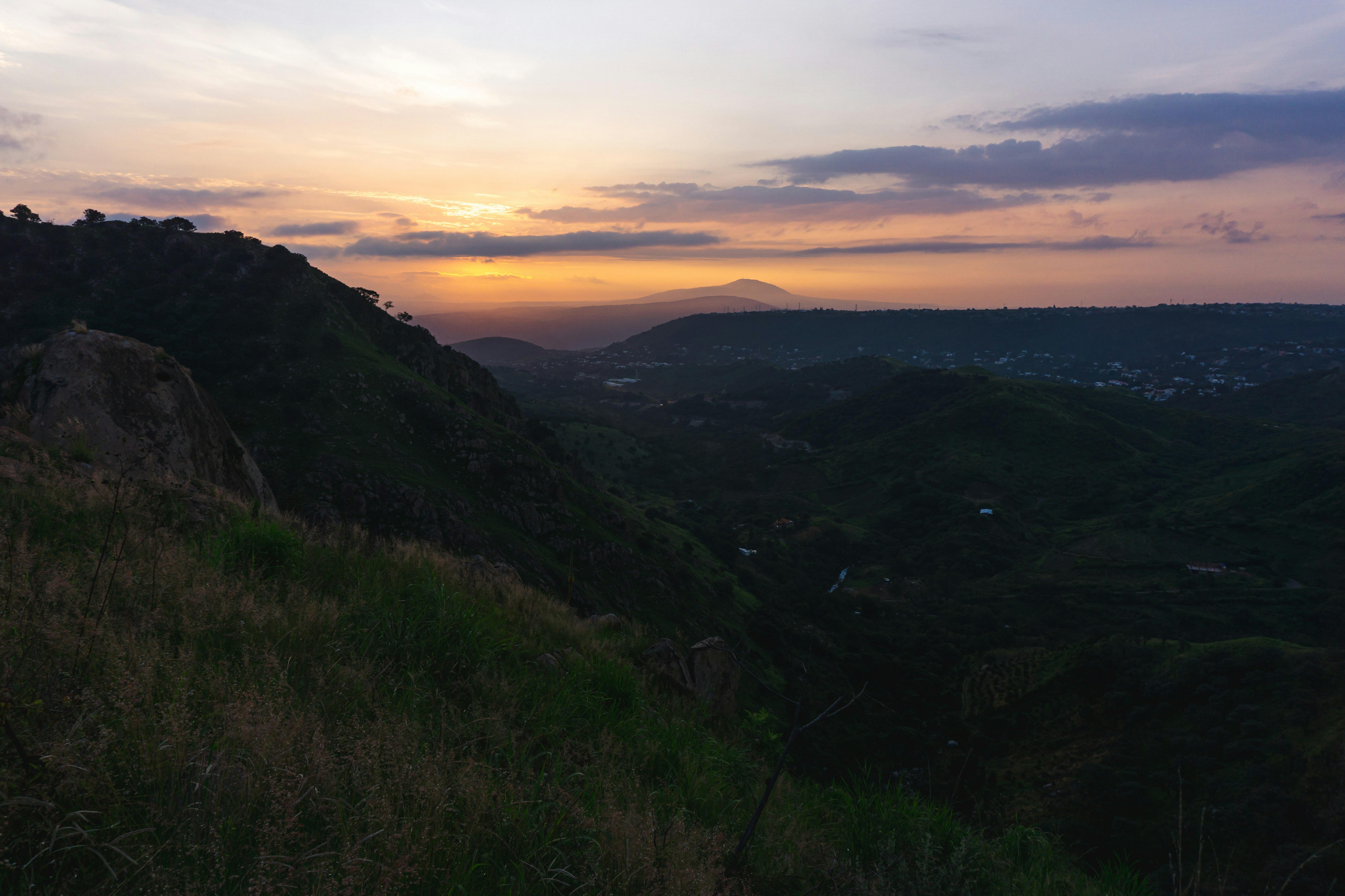 Sunset over rolling hills and distant mountains under a colorful sky.