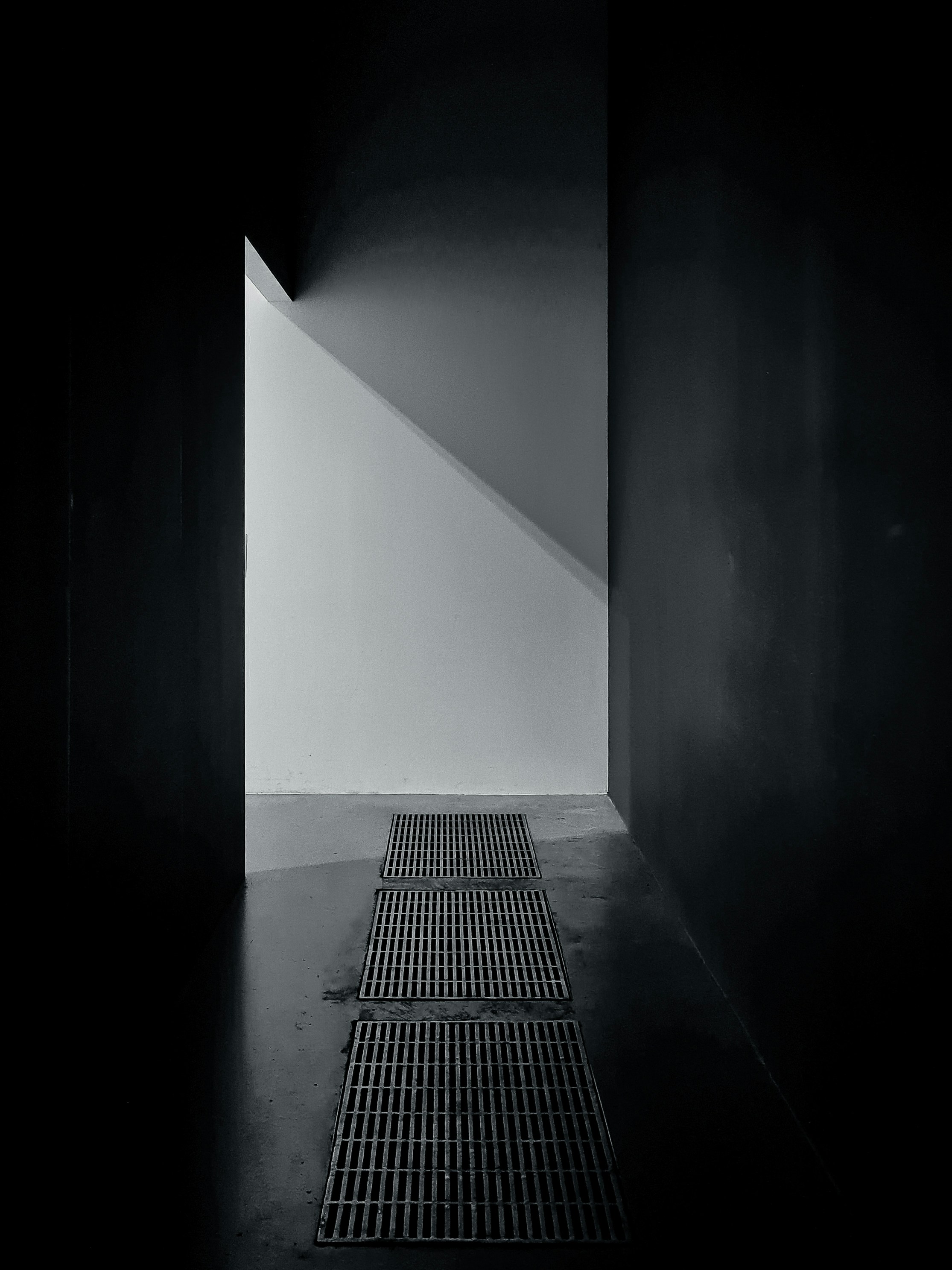 A narrow corridor illuminated by a beam of light, leading to an open space. The contrast between dark walls and the bright floor creates a striking visual effect.