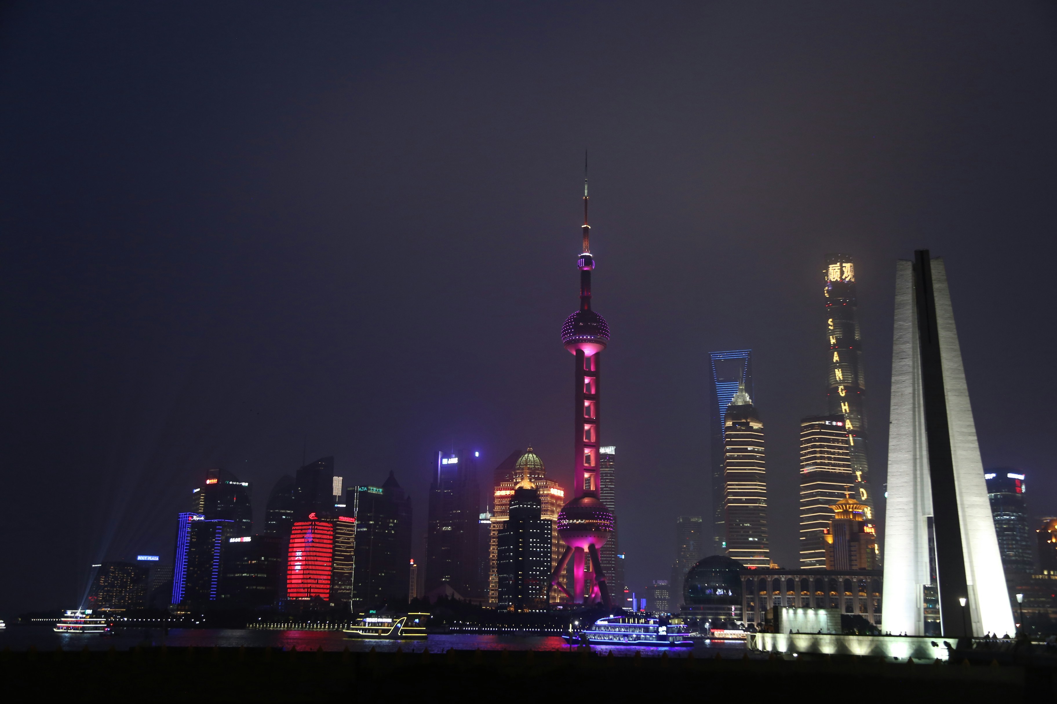 Shanghai skyline at night with vibrant skyscrapers and illuminated boats on the river.