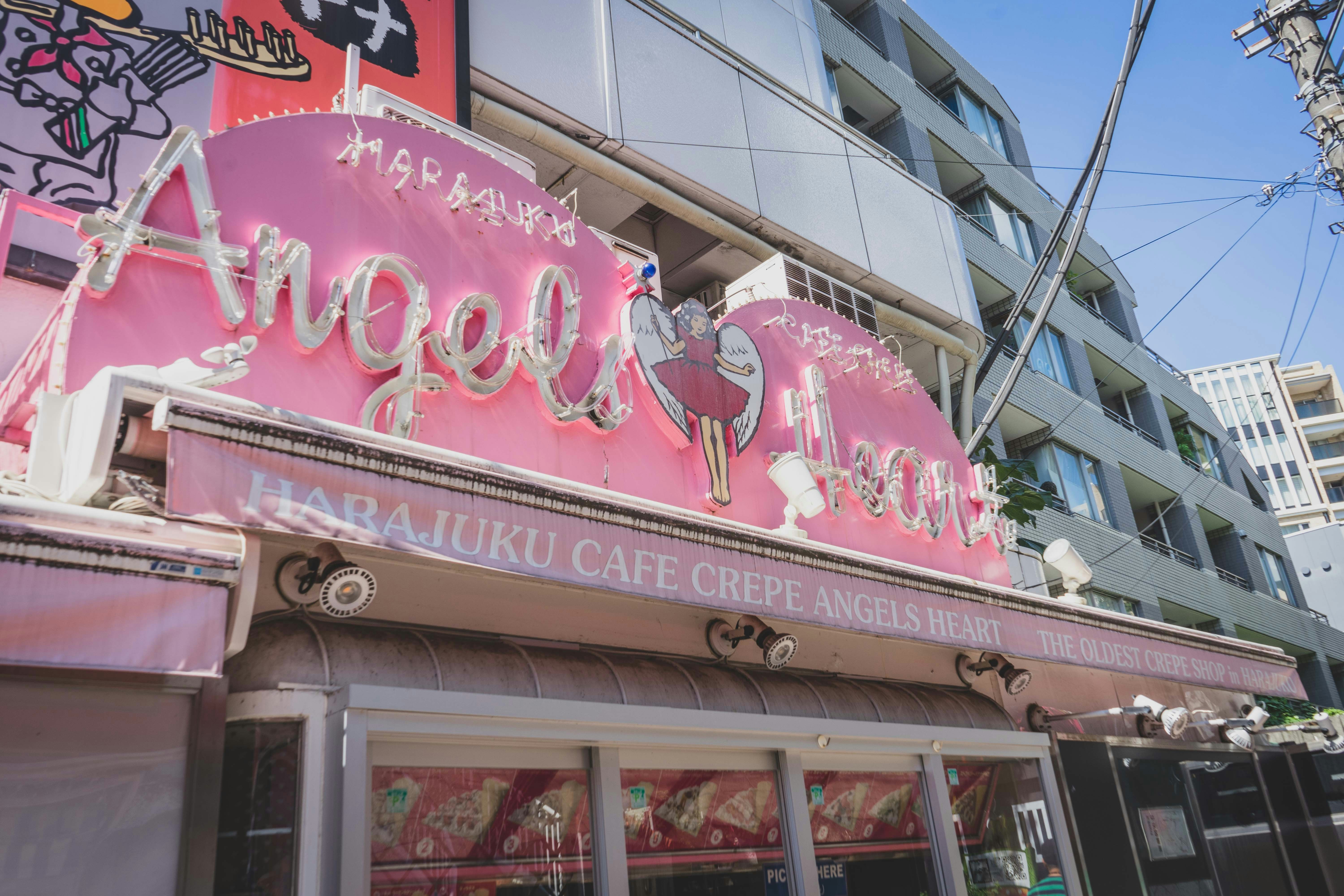 Sunlit Pink Signage of Angels Heart Café on a Busy Street